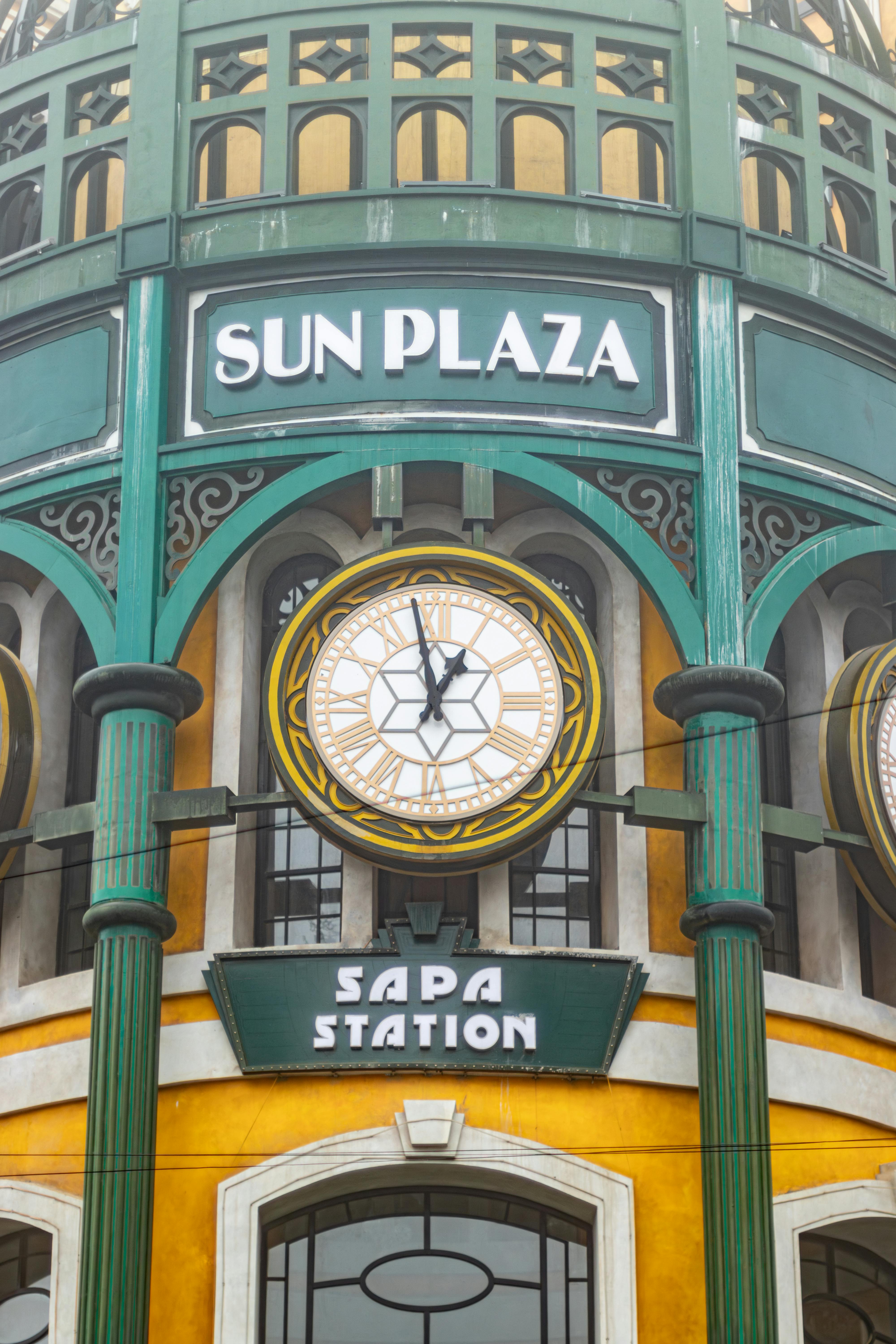 A clock tower with a large sun plaza sign on it · Free Stock Photo