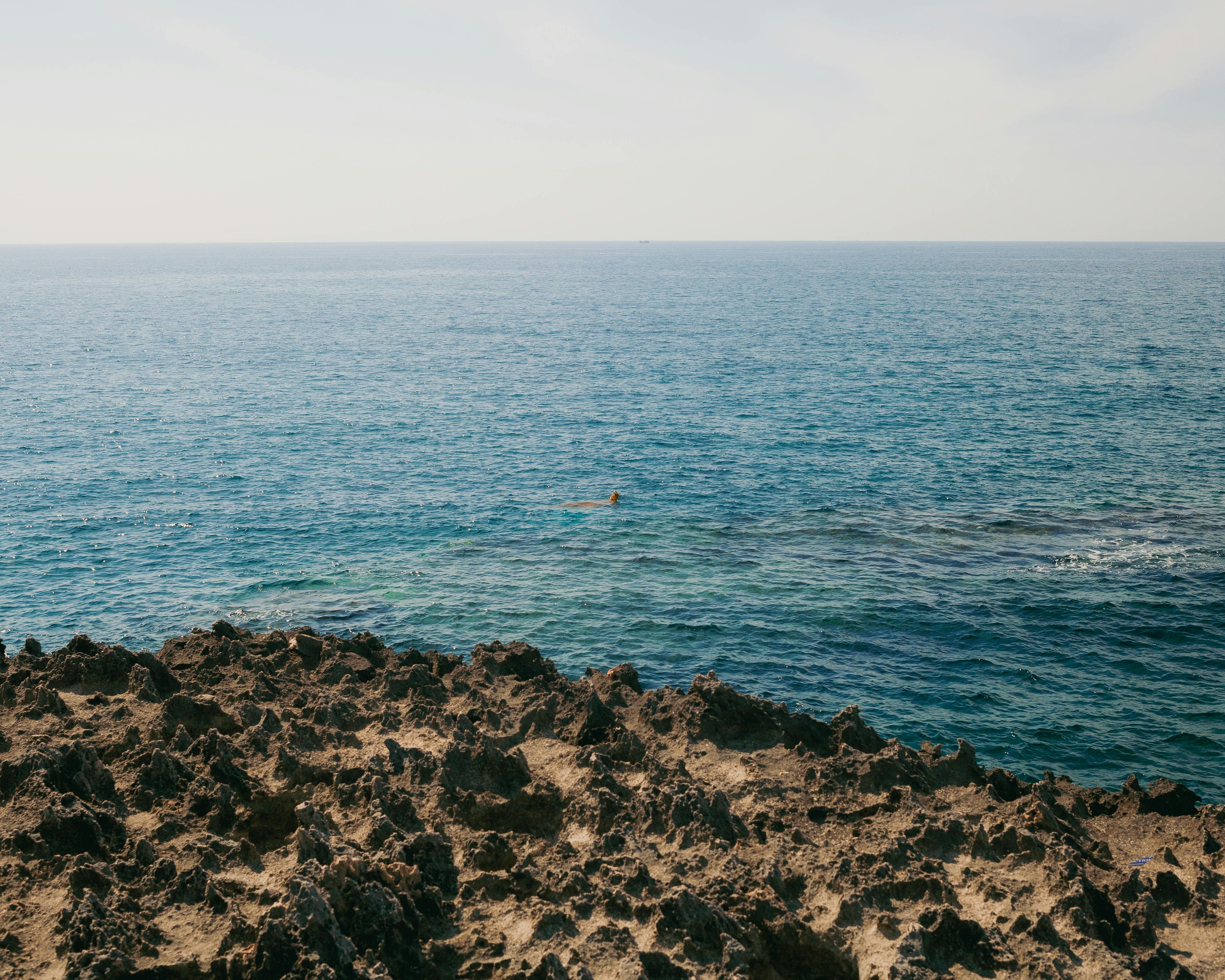 A person is swimming in the ocean near a rocky shore · Free Stock Photo