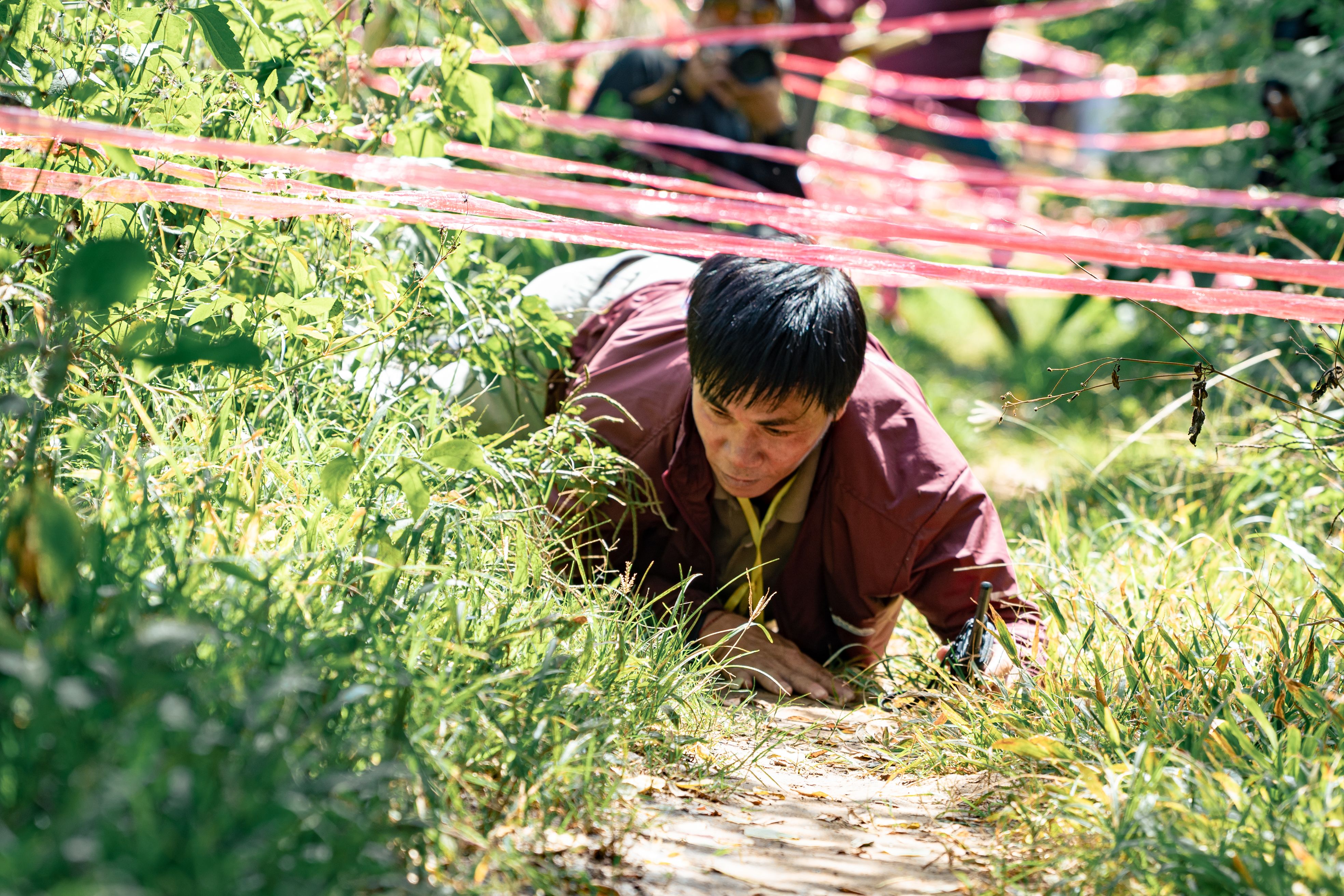 A man crawling through a forest with pink tape · Free Stock Photo