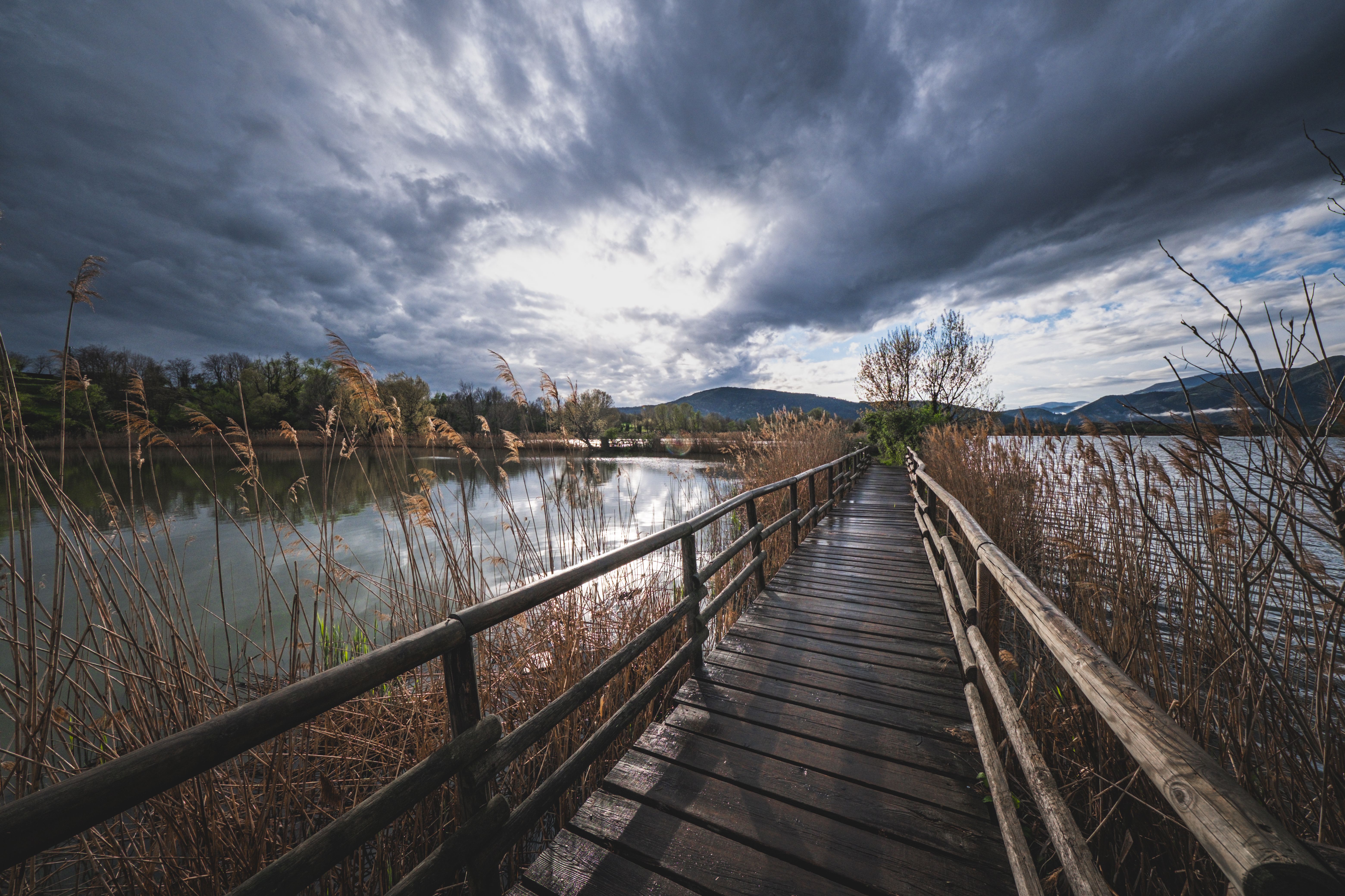A wooden walkway over a lake with storm clouds · Free Stock Photo