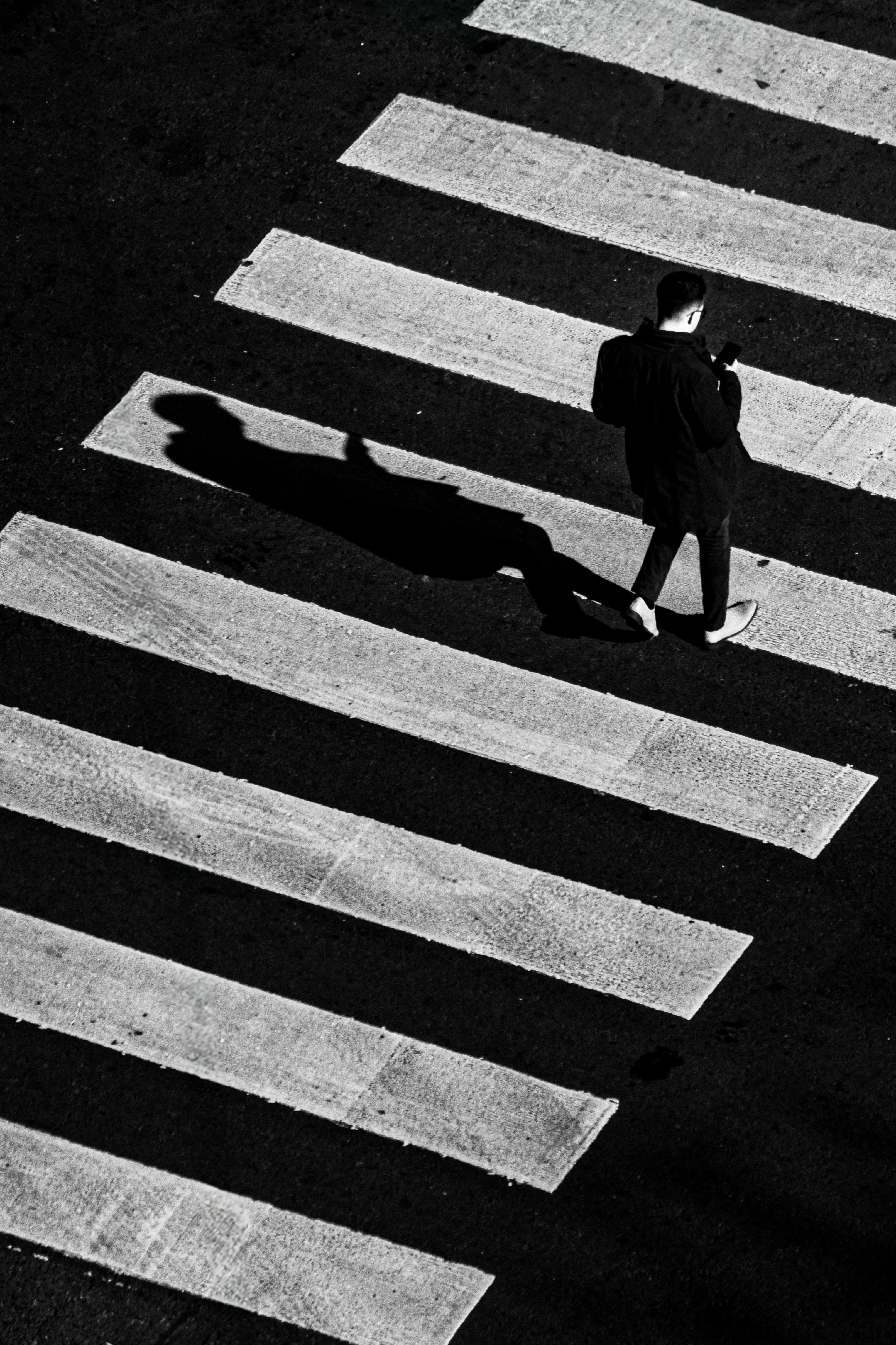 A black and white photo of a person walking across a crosswalk · Free ...