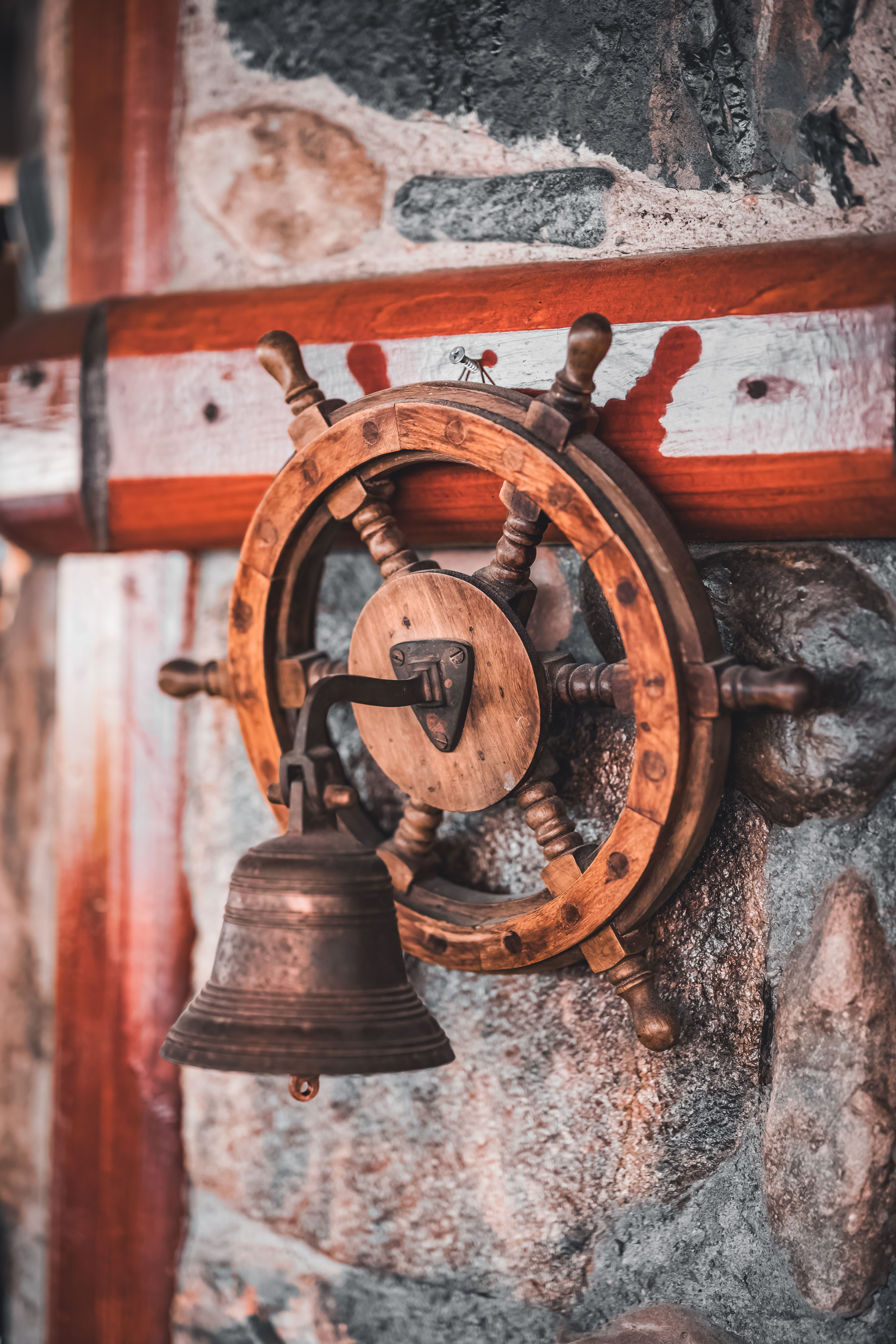 A ship's wheel and bell on a wall · Free Stock Photo