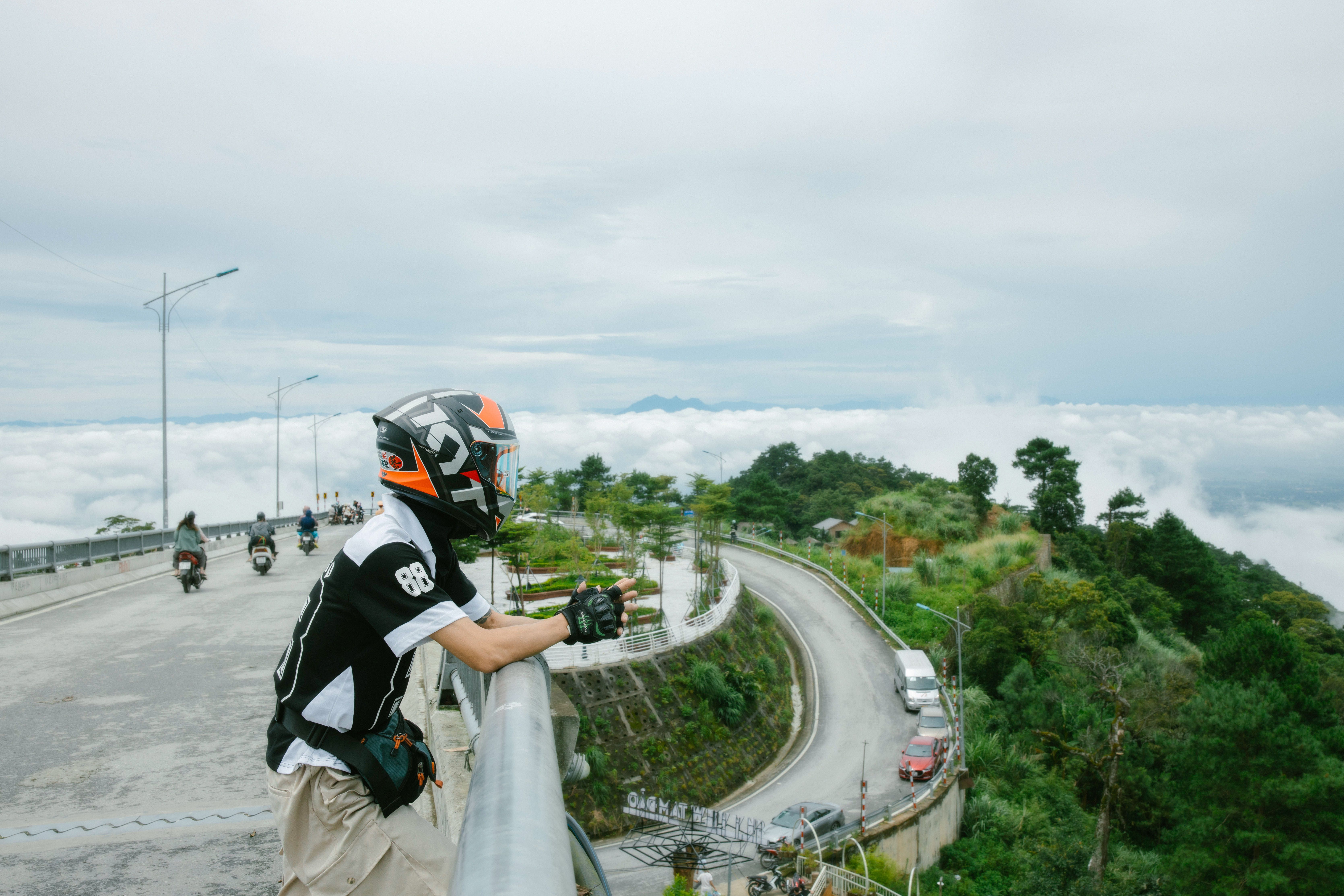A man on a motorcycle looking over the edge of a bridge · Free Stock Photo