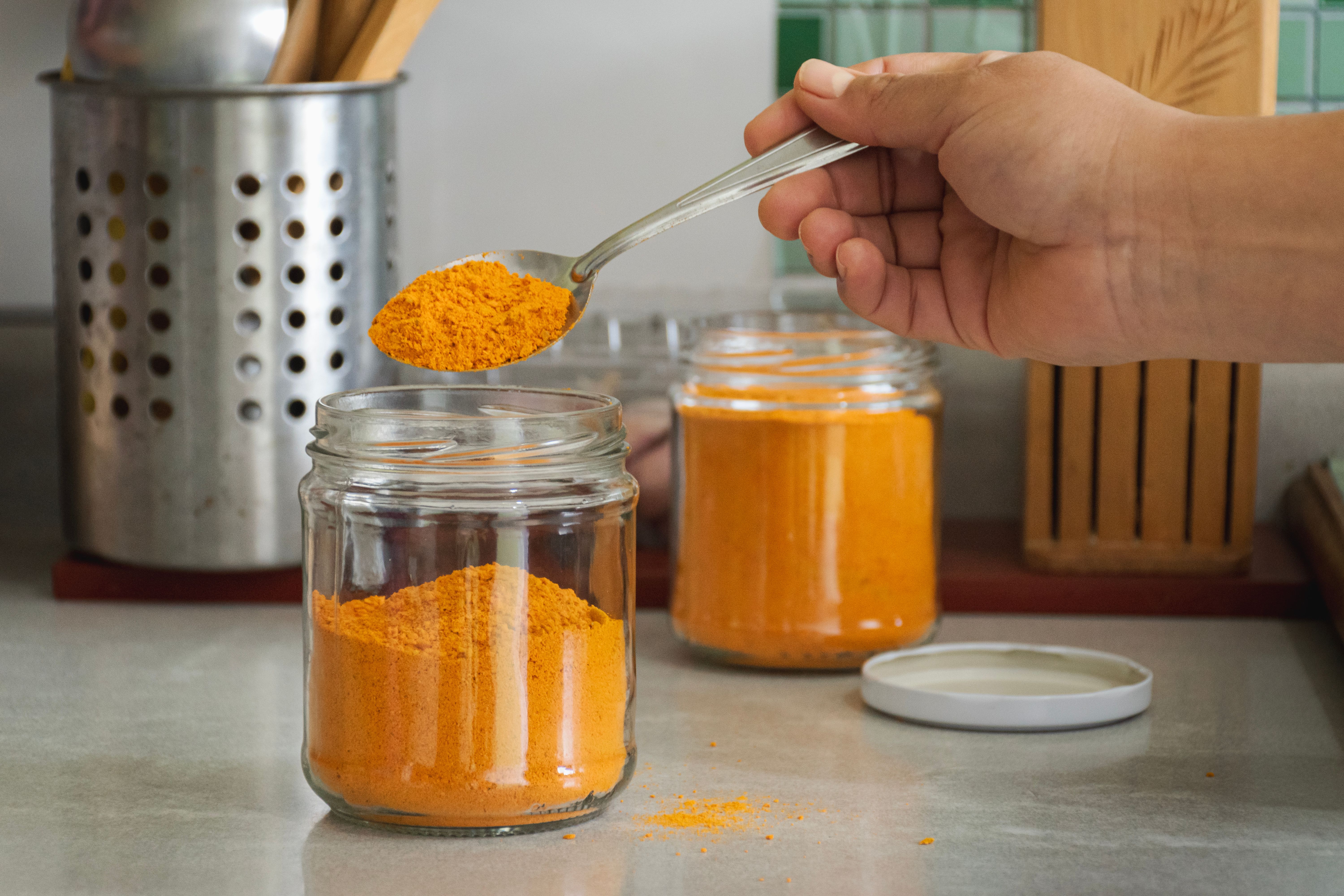 A person is holding a spoon over a jar of orange powder · Free Stock Photo
