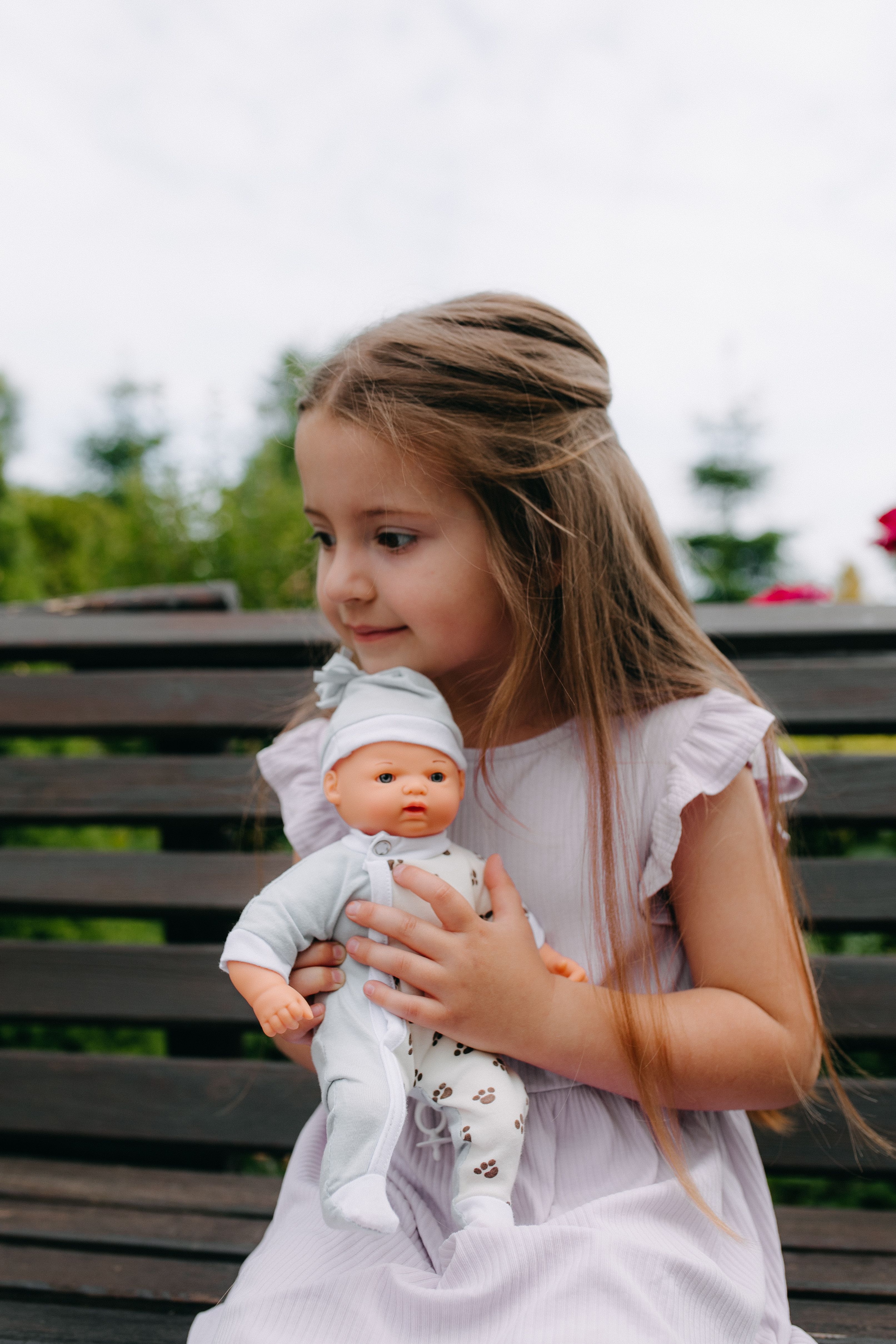 A little girl holding a doll on a bench · Free Stock Photo