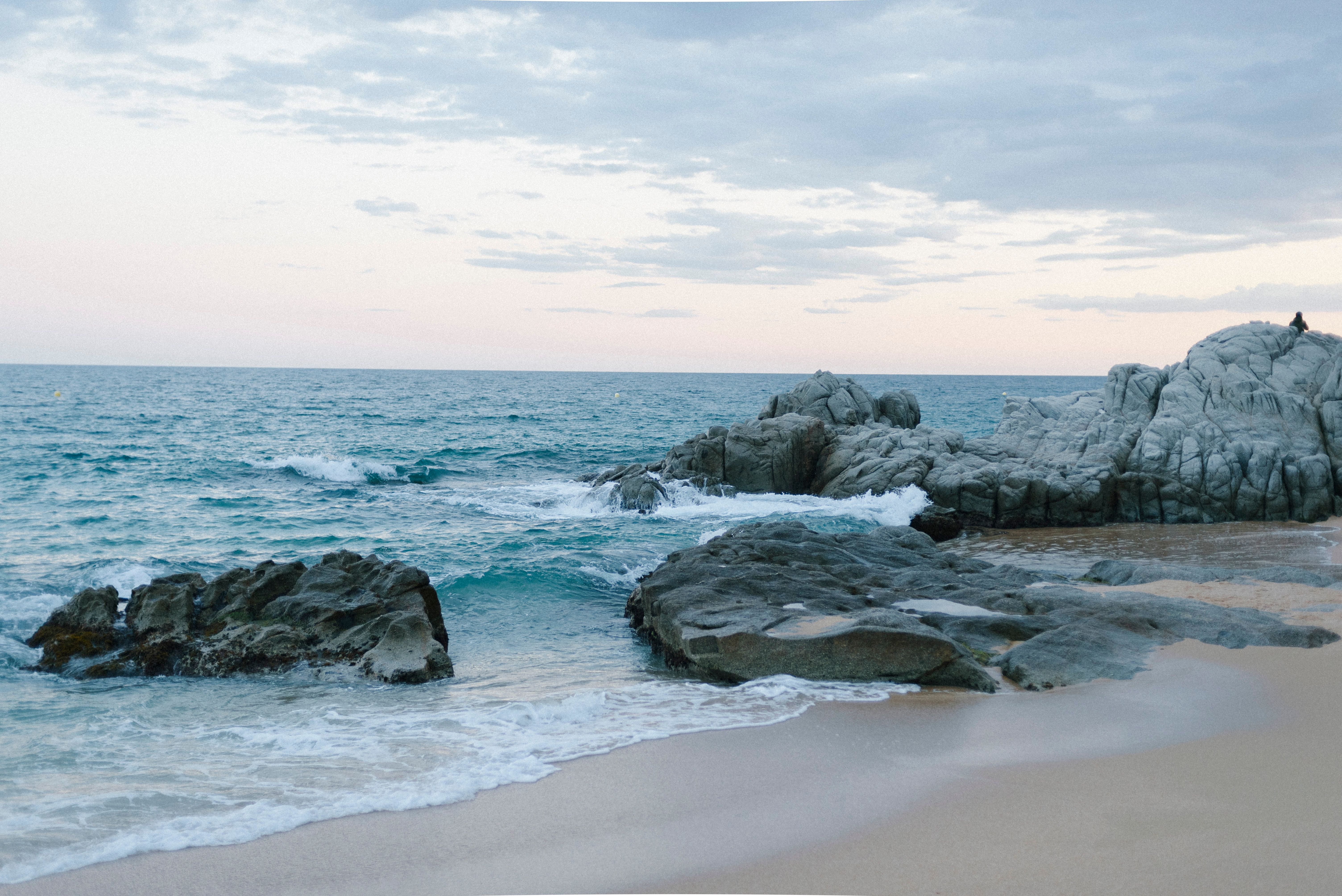 A beach with rocks and water at sunset · Free Stock Photo