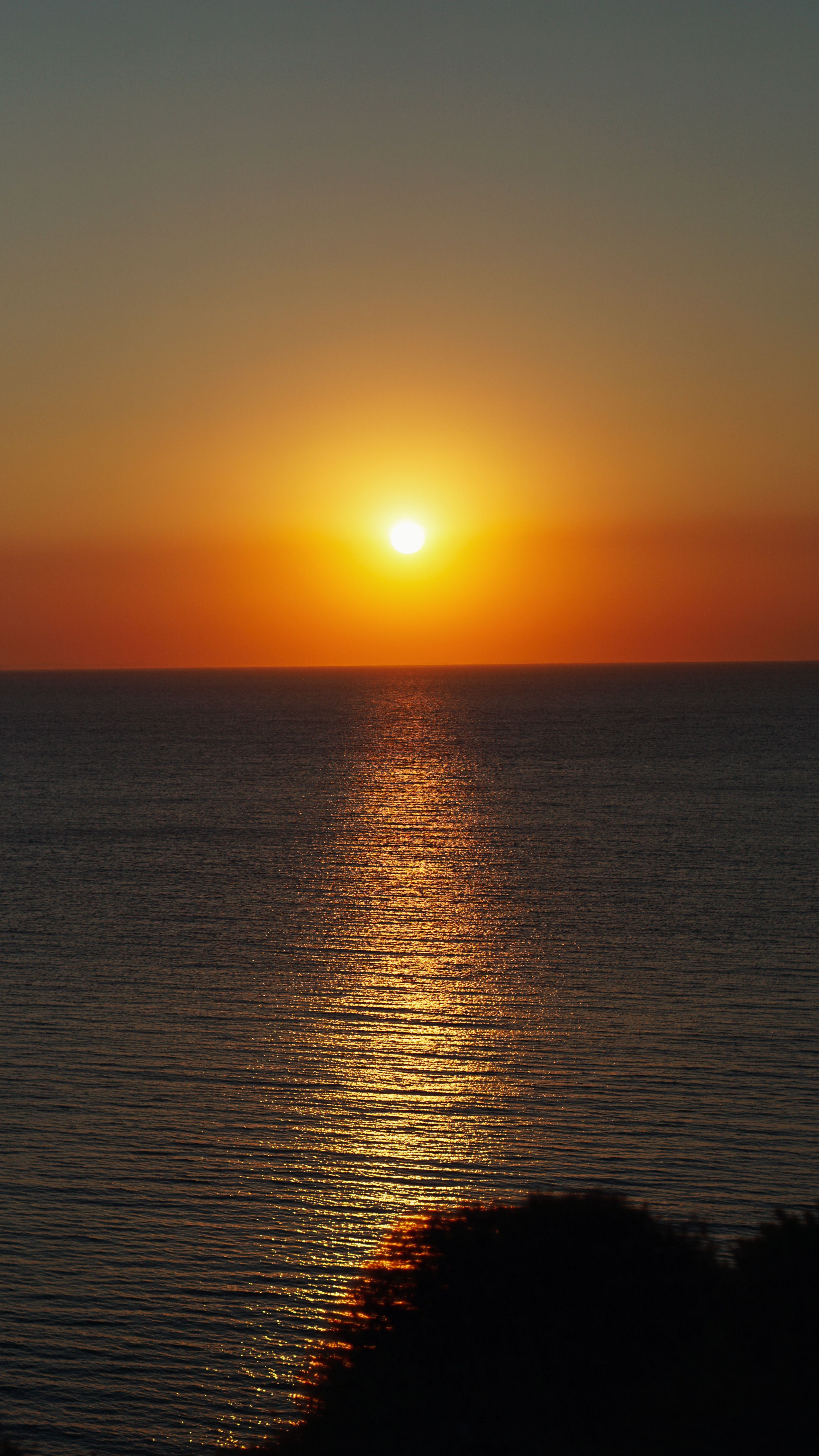 A sunset over the ocean with a bright orange sun · Free Stock Photo