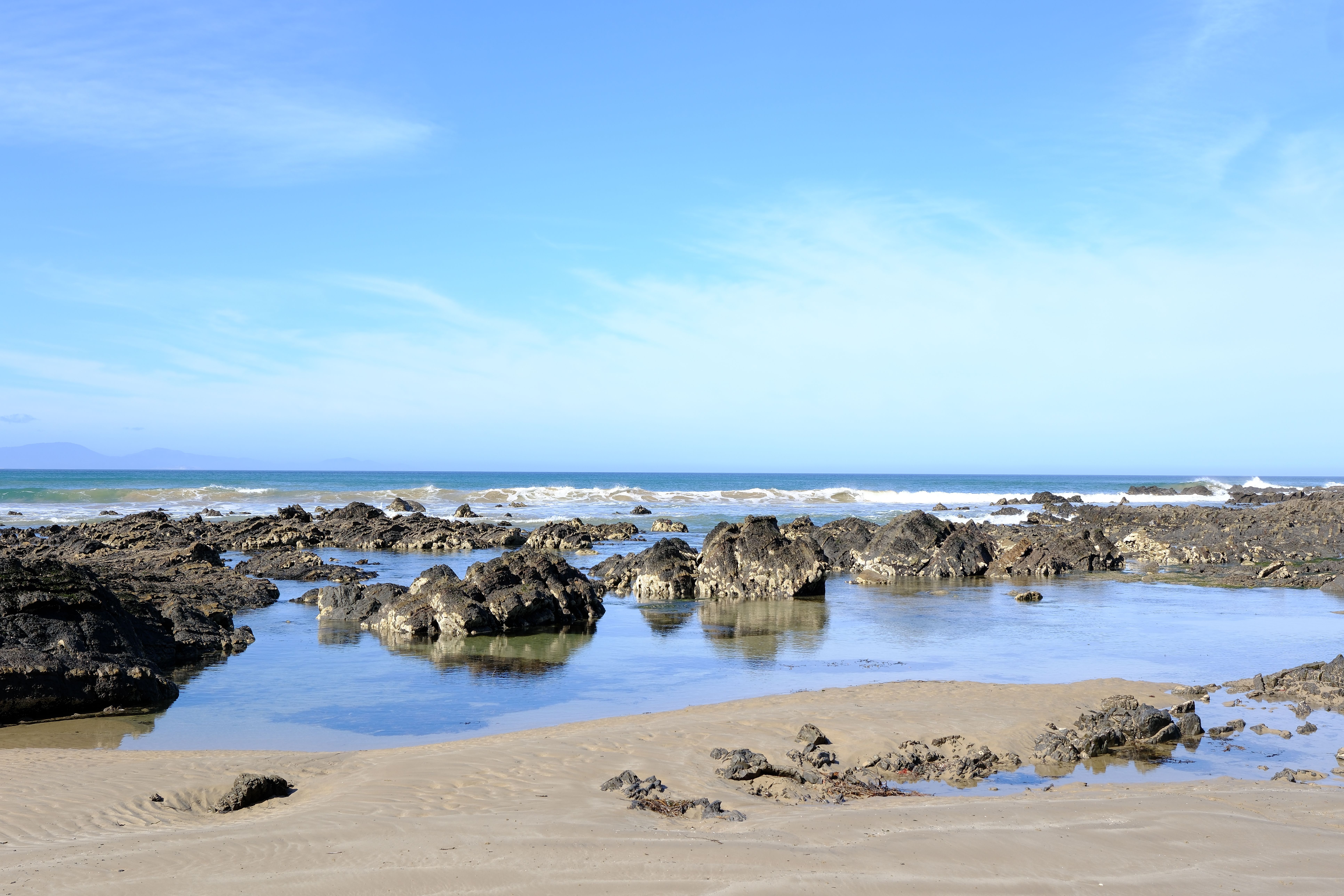 A beach with rocks and water in the background · Free Stock Photo