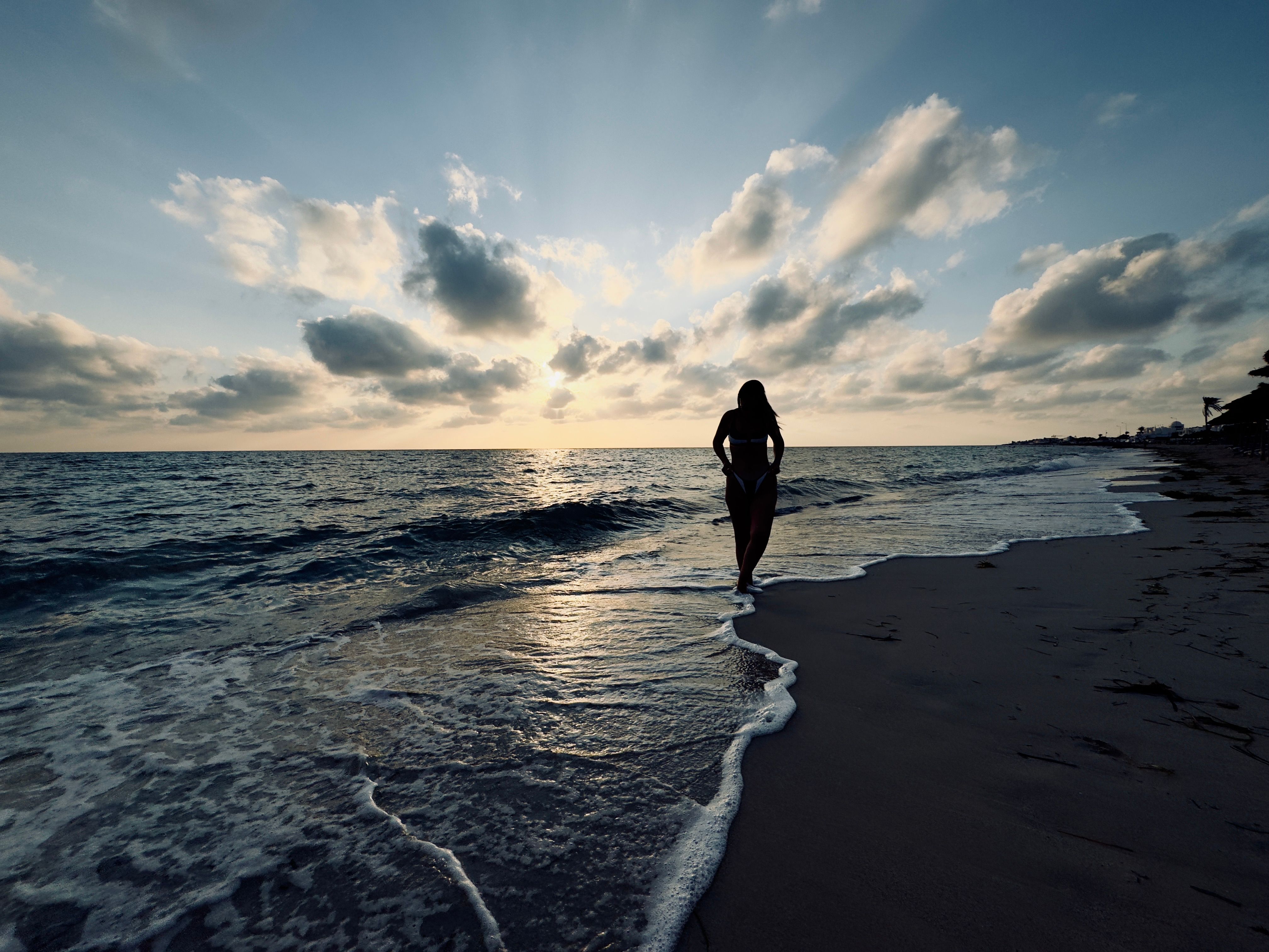 A woman walking on the beach at sunset · Free Stock Photo