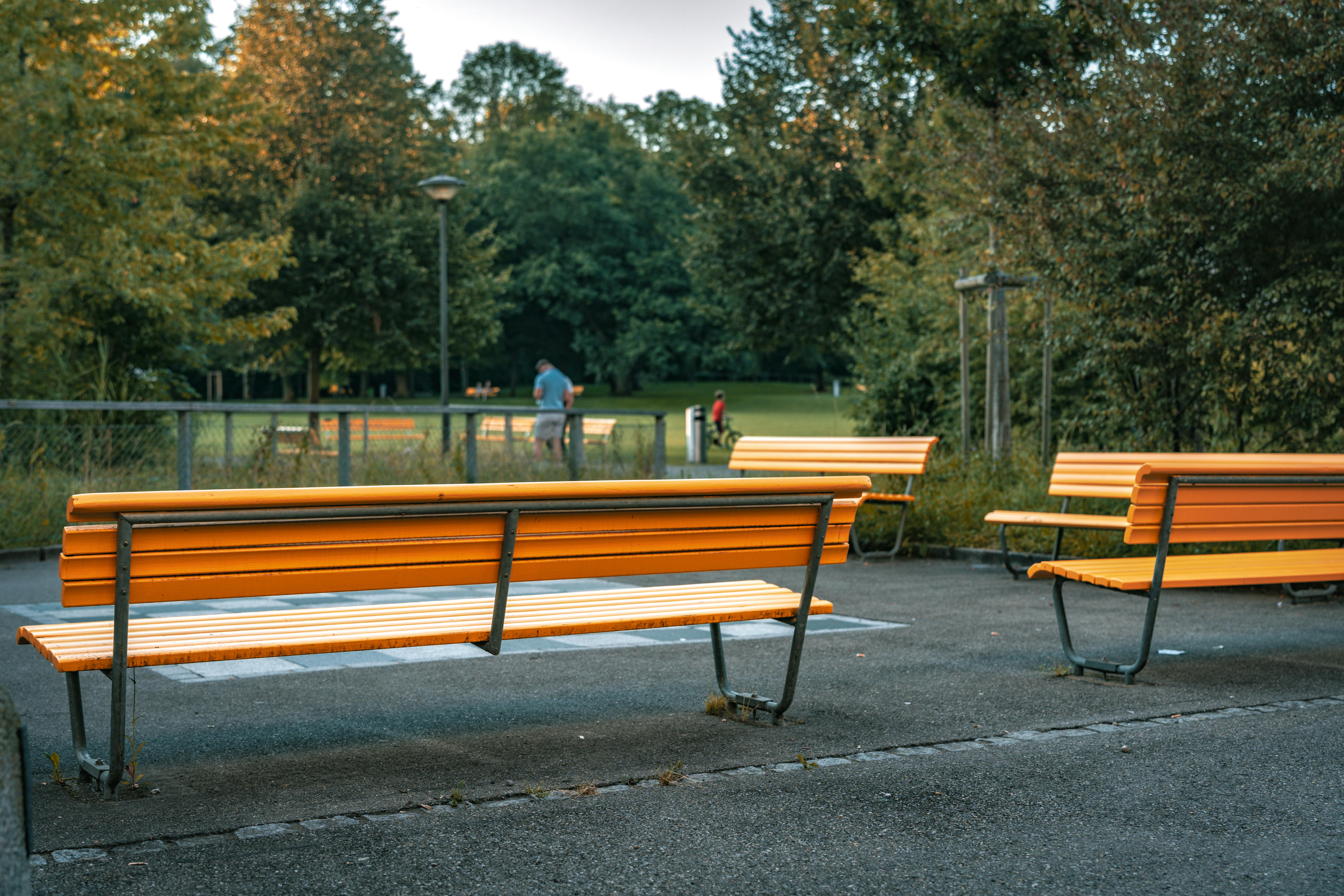 Two orange benches in a park with people walking by · Free Stock Photo