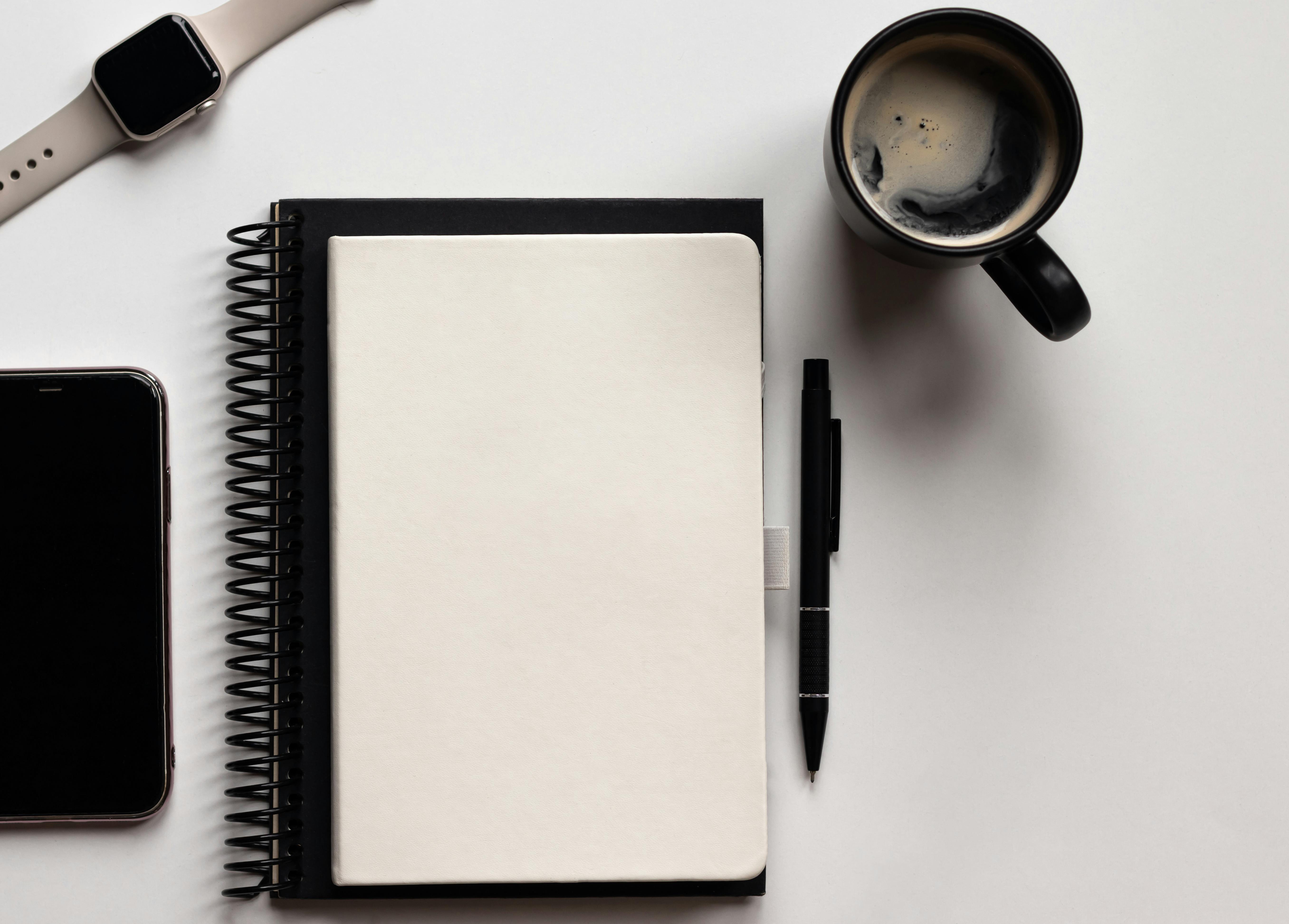 A notebook, phone and coffee cup on a white table · Free Stock Photo