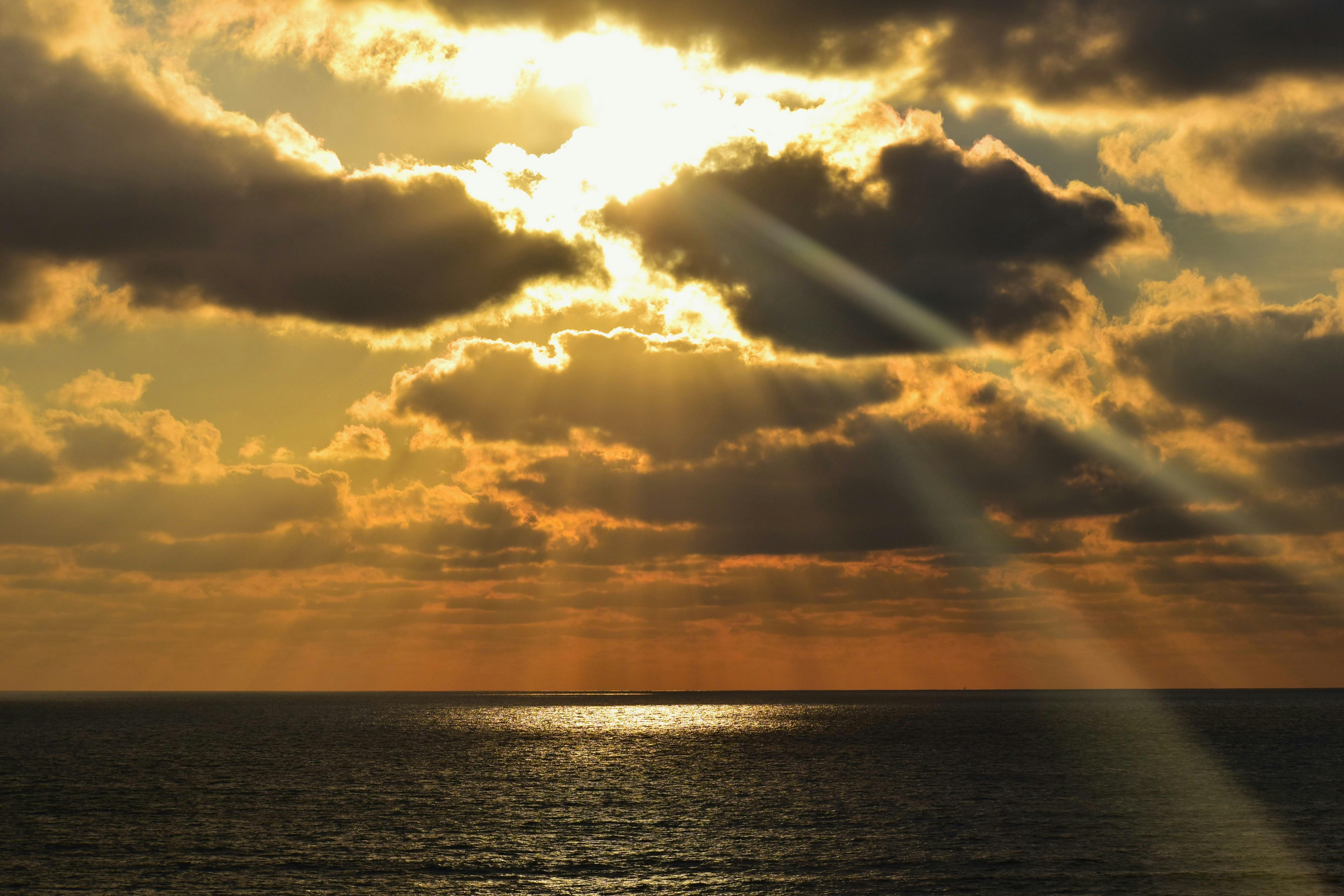 Sun rays shining through clouds over the ocean · Free Stock Photo