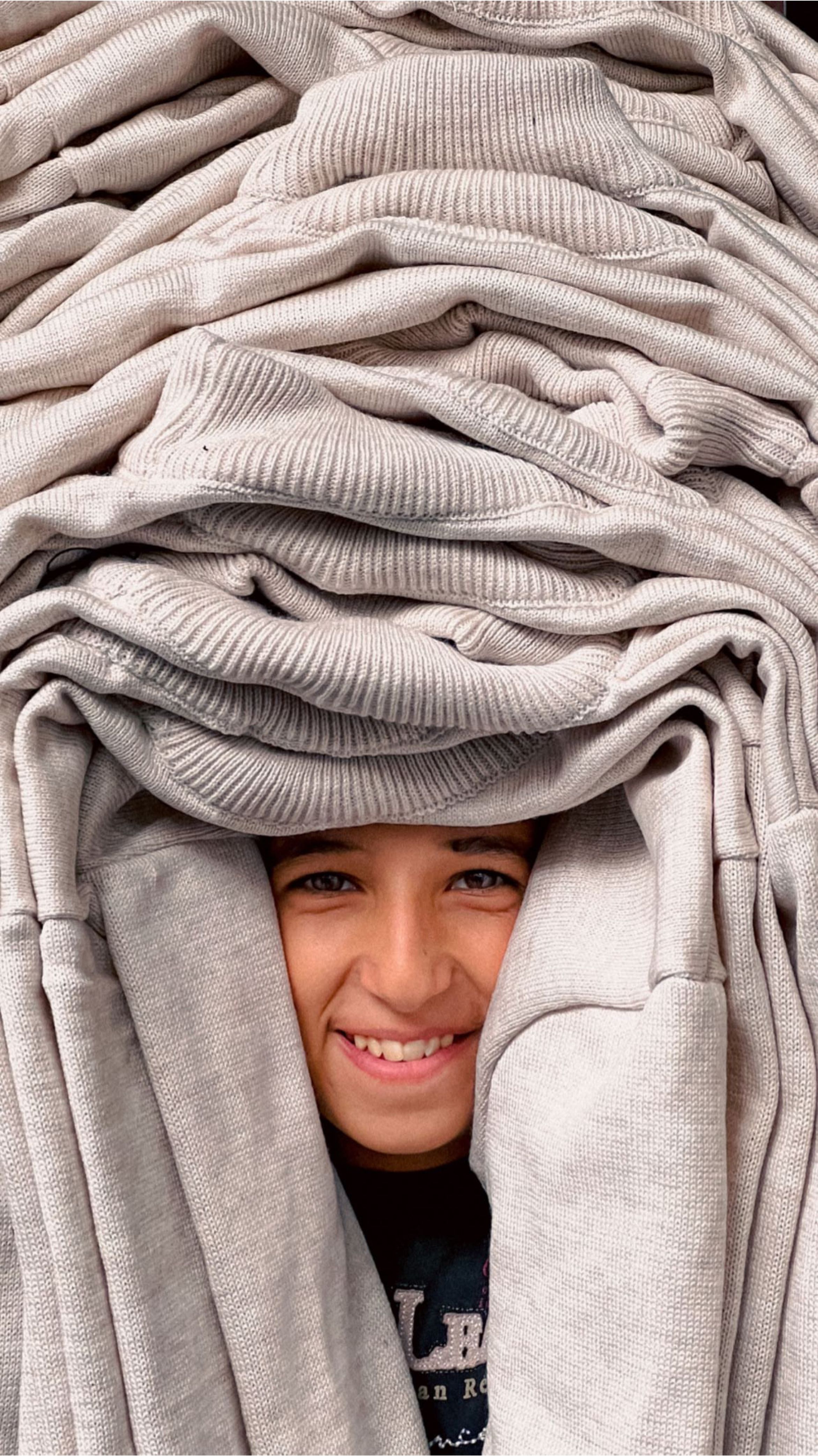 A young boy is smiling while hiding under a pile of clothes · Free ...