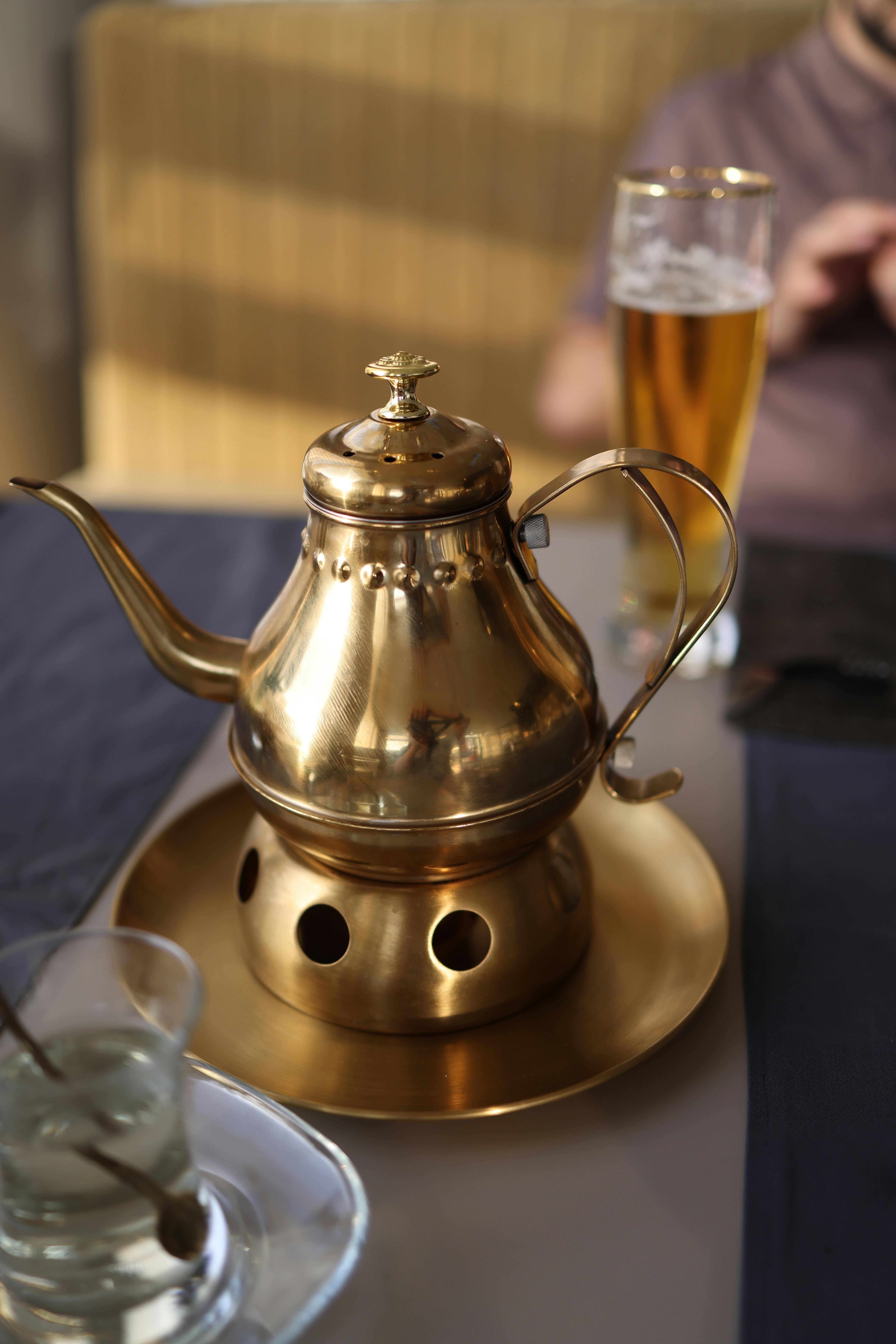 A gold teapot on a table with a glass of beer · Free Stock Photo