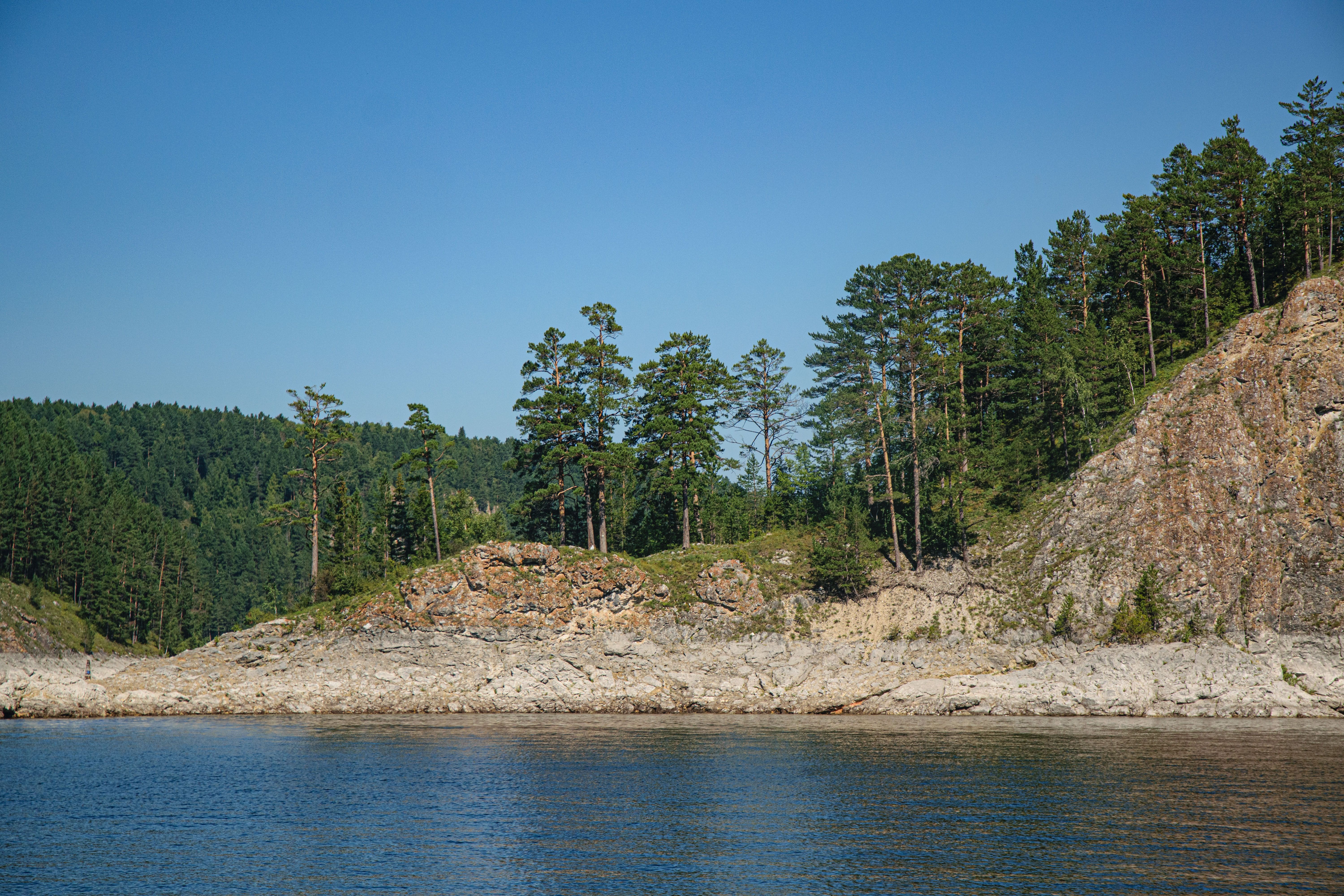 A rocky shoreline with trees and a small lake · Free Stock Photo