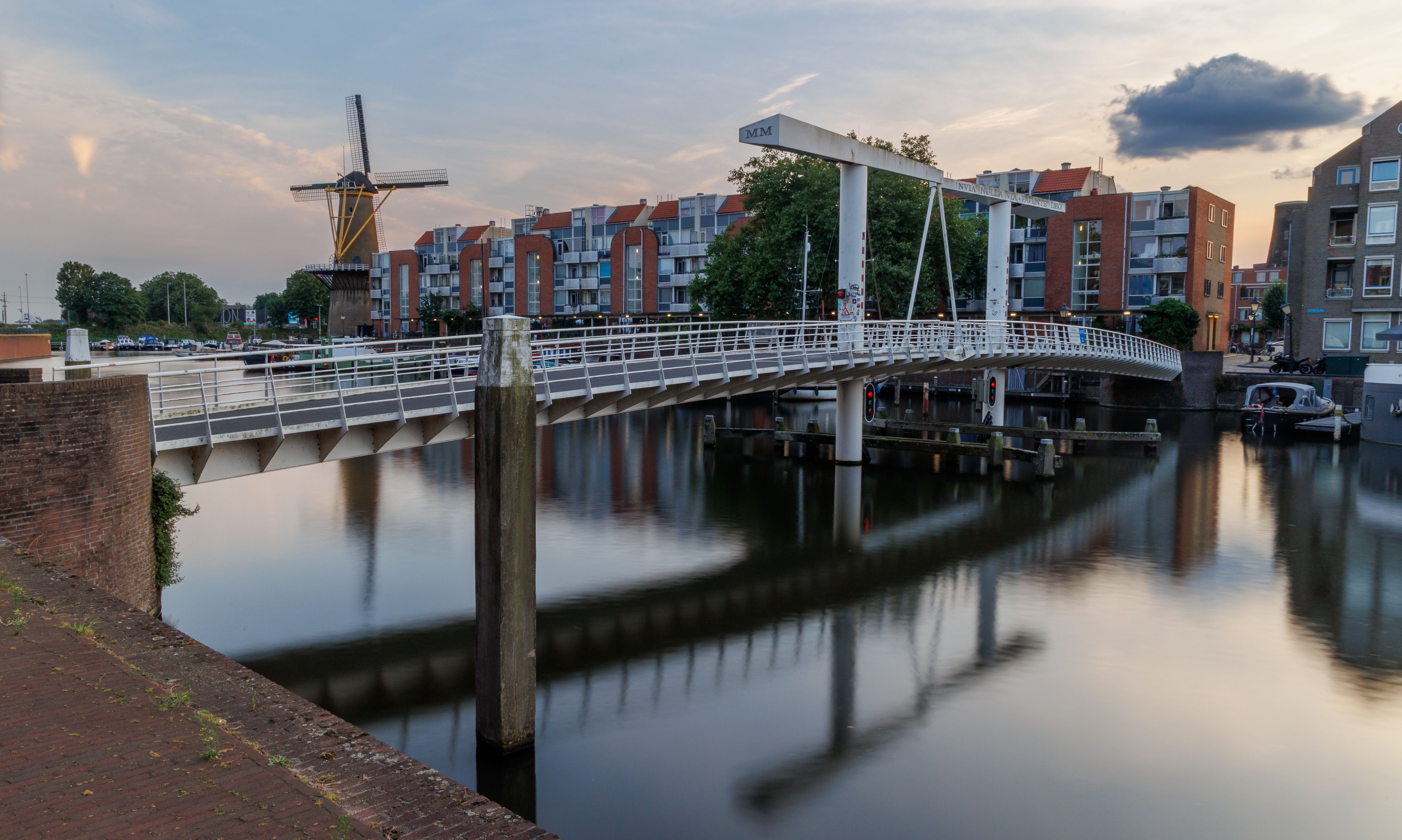 A bridge over a canal with a windmill in the background · Free Stock Photo
