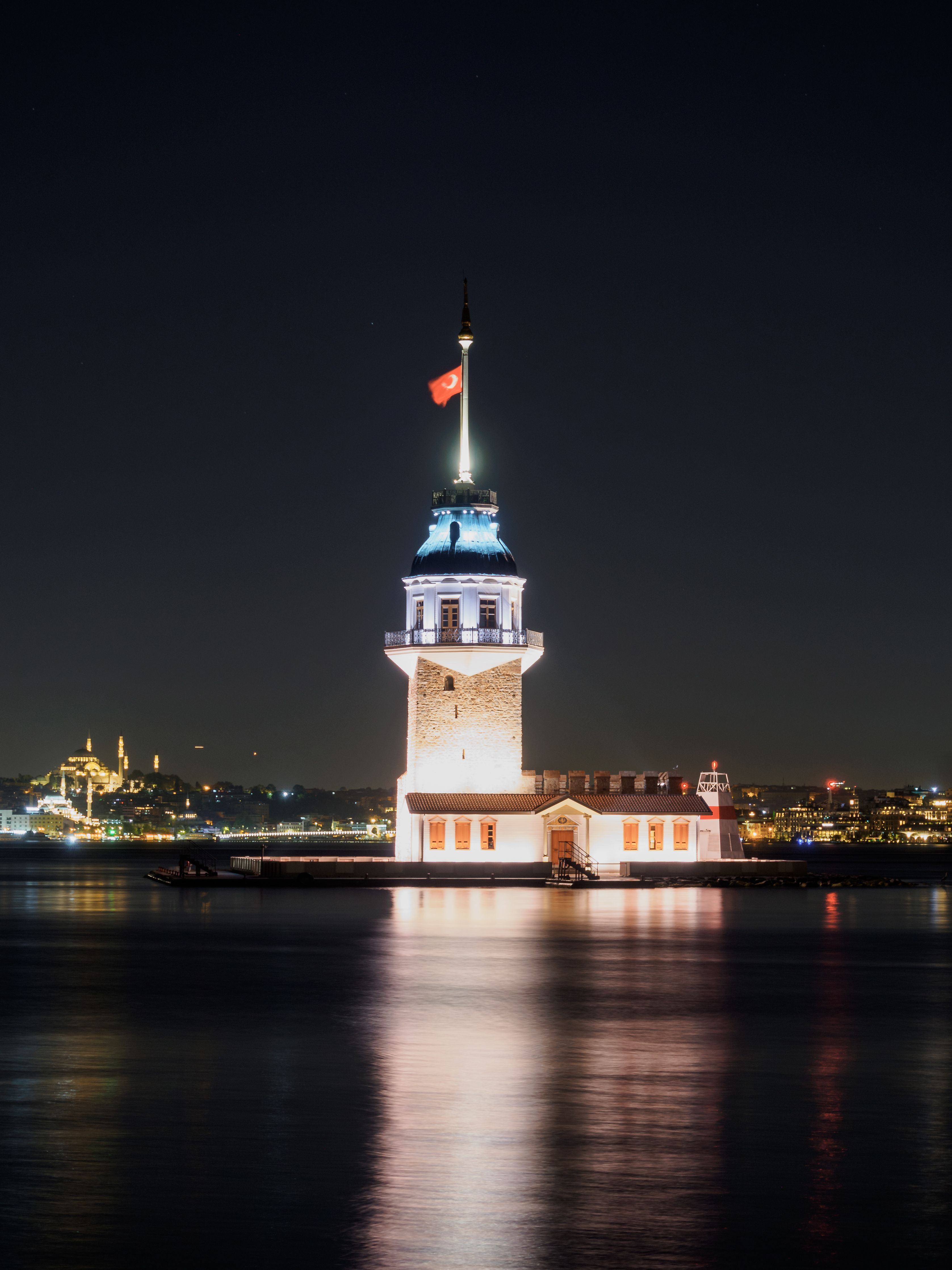 A tower lit up at night on the water · Free Stock Photo