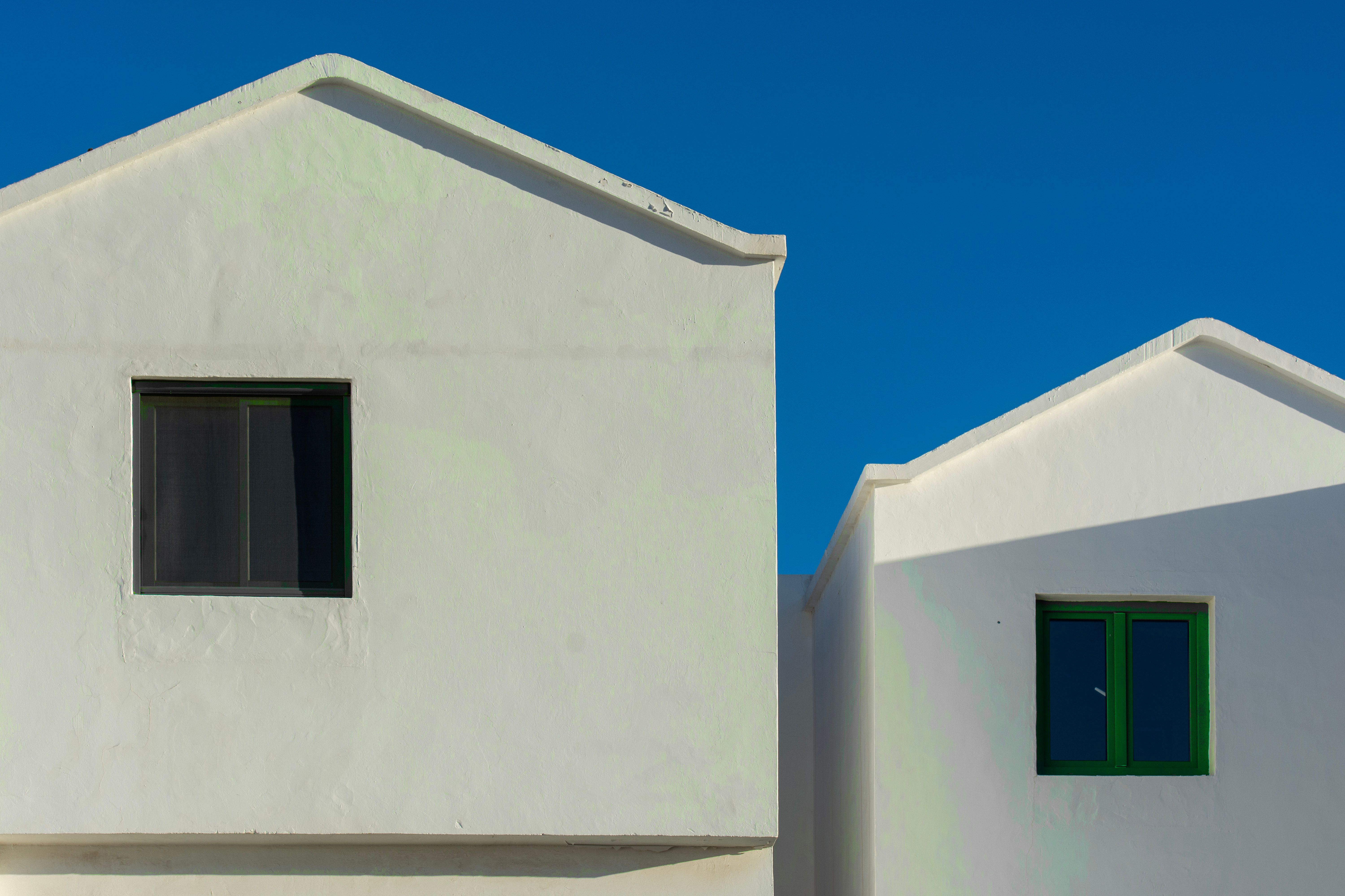 Two white houses with green windows and a blue sky · Free Stock Photo