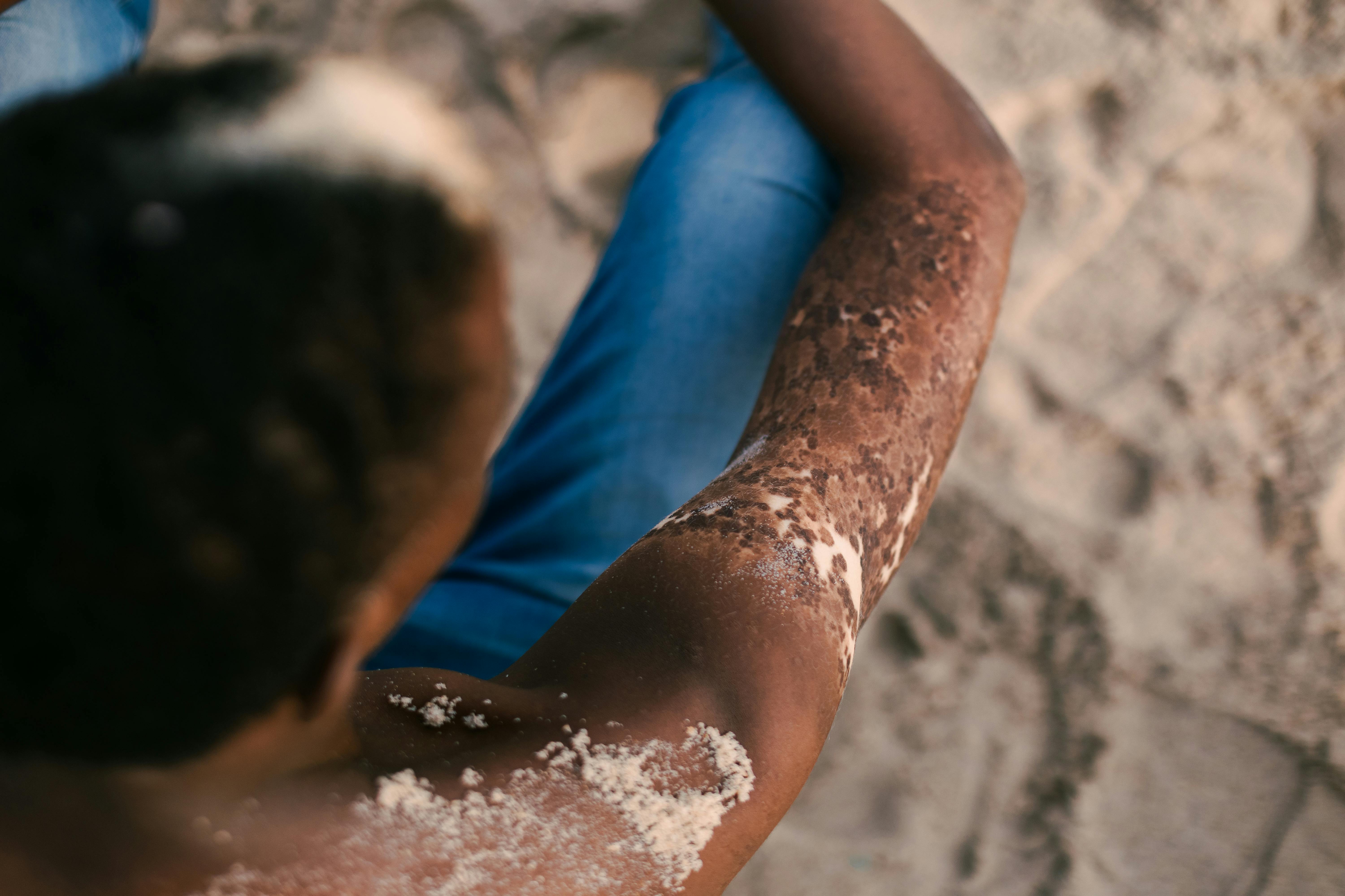 A person sitting on the sand with a white arm · Free Stock Photo