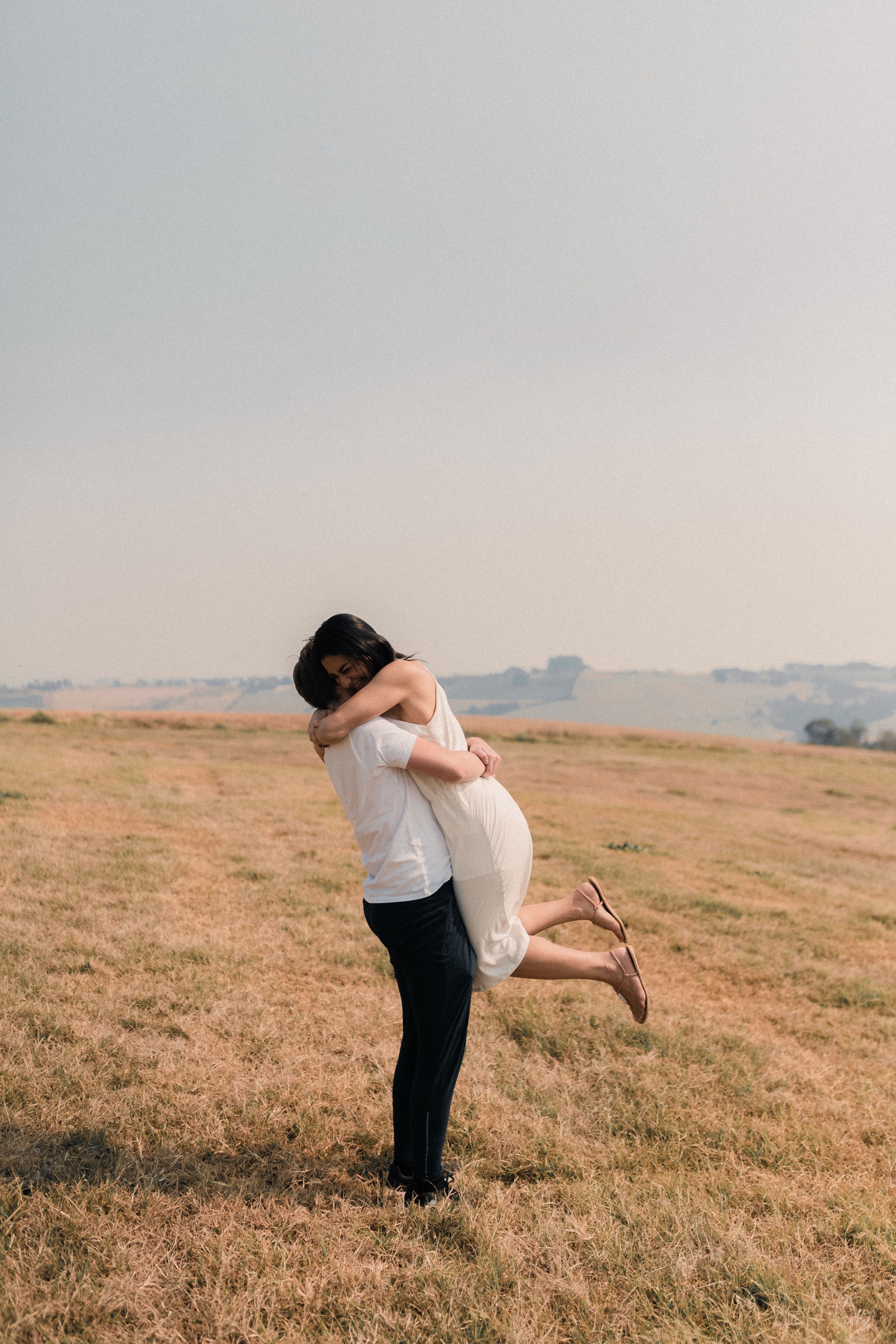 A couple hugging in the grass in front of a field · Free Stock Photo