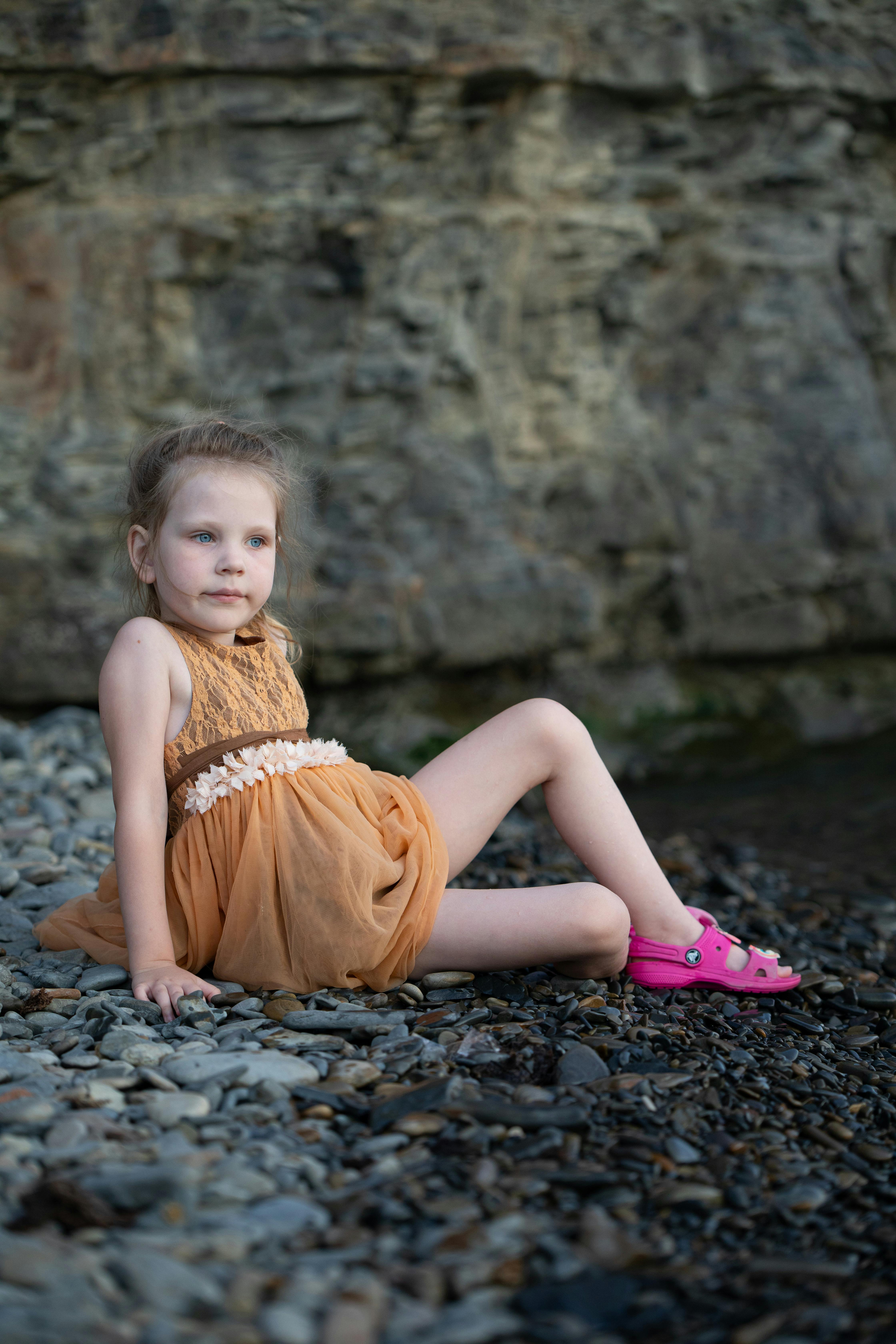 A little girl sitting on the rocks in a dress · Free Stock Photo