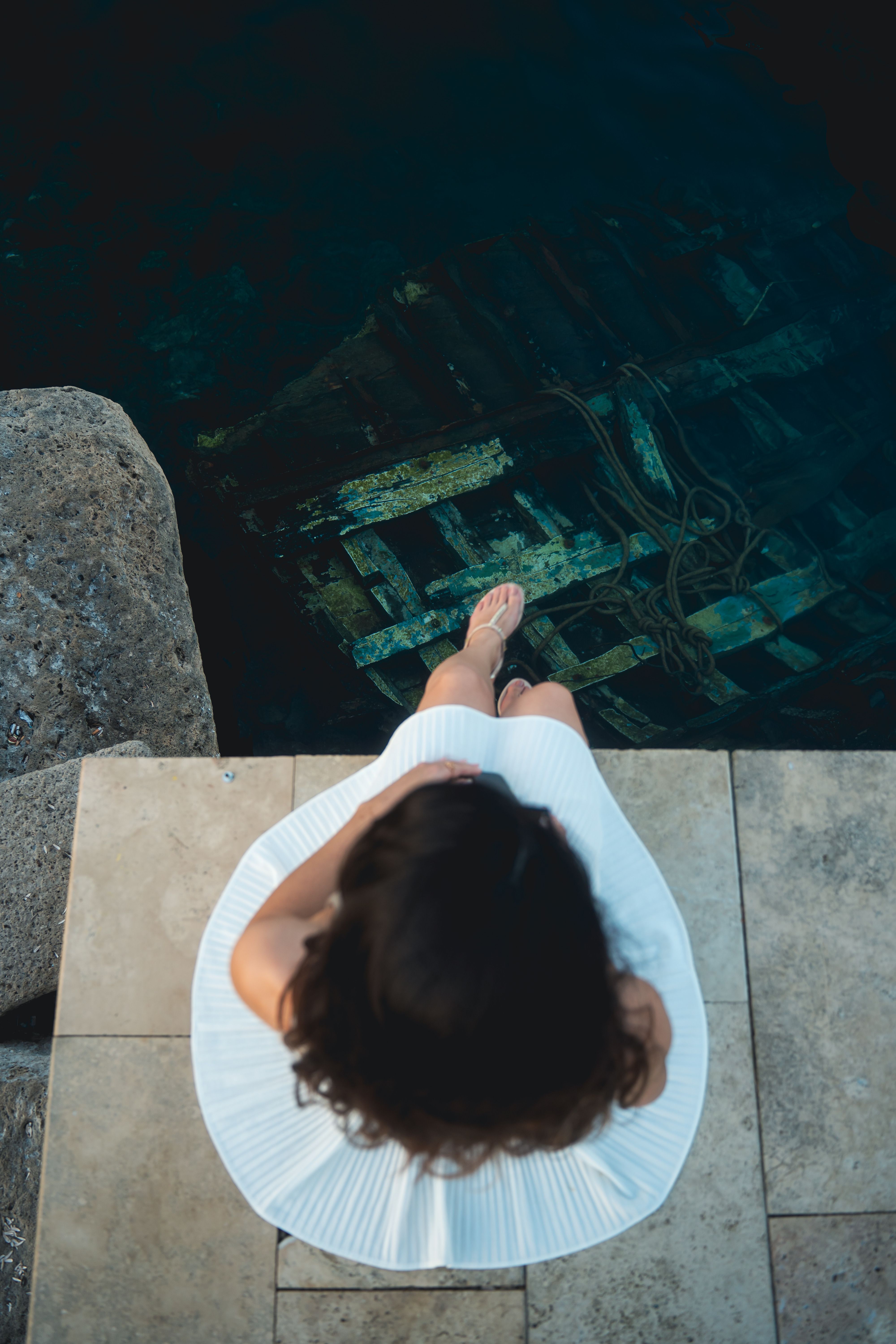 A woman sitting on a ledge looking at the water · Free Stock Photo