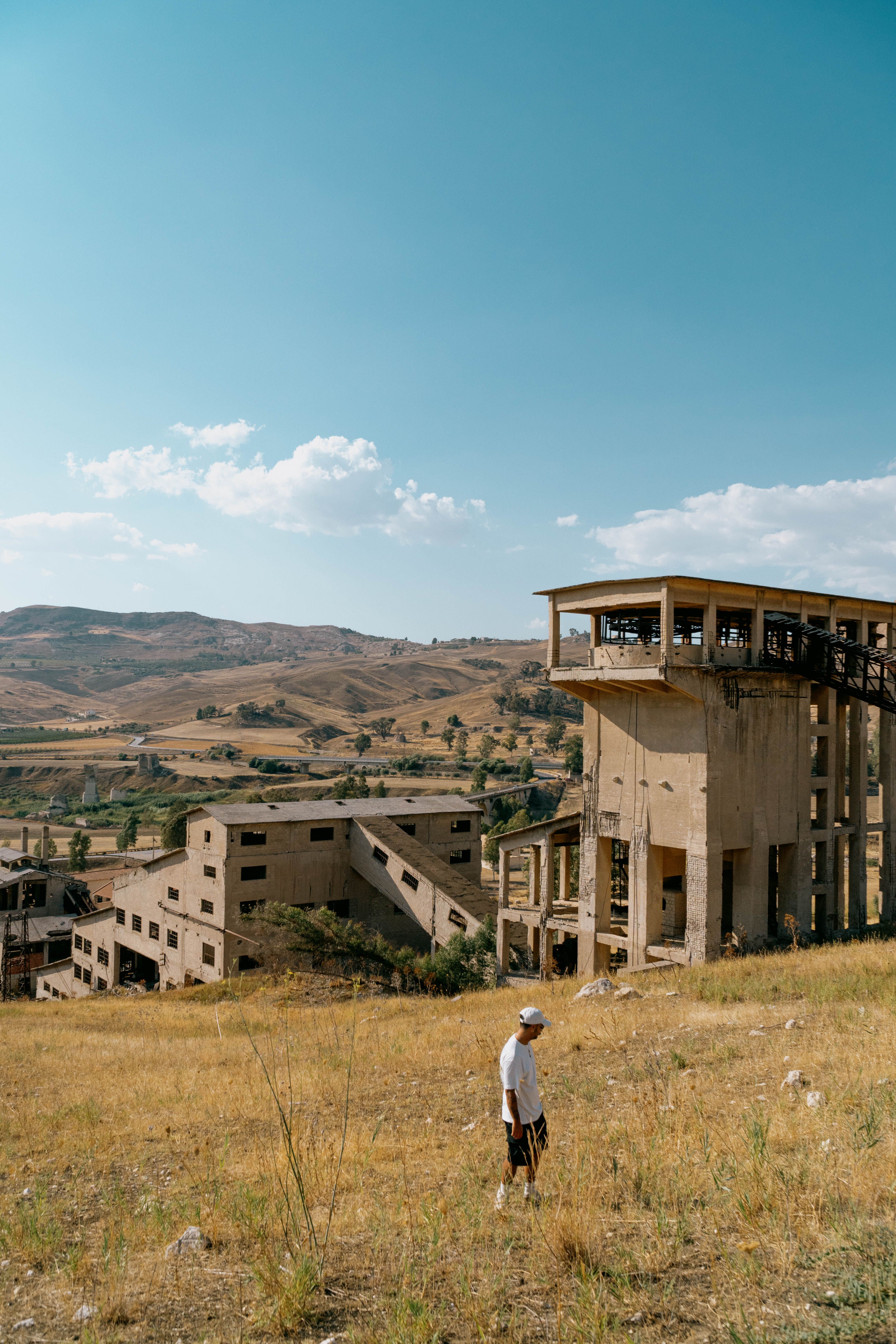 A man walking on a hillside near an abandoned building · Free Stock Photo