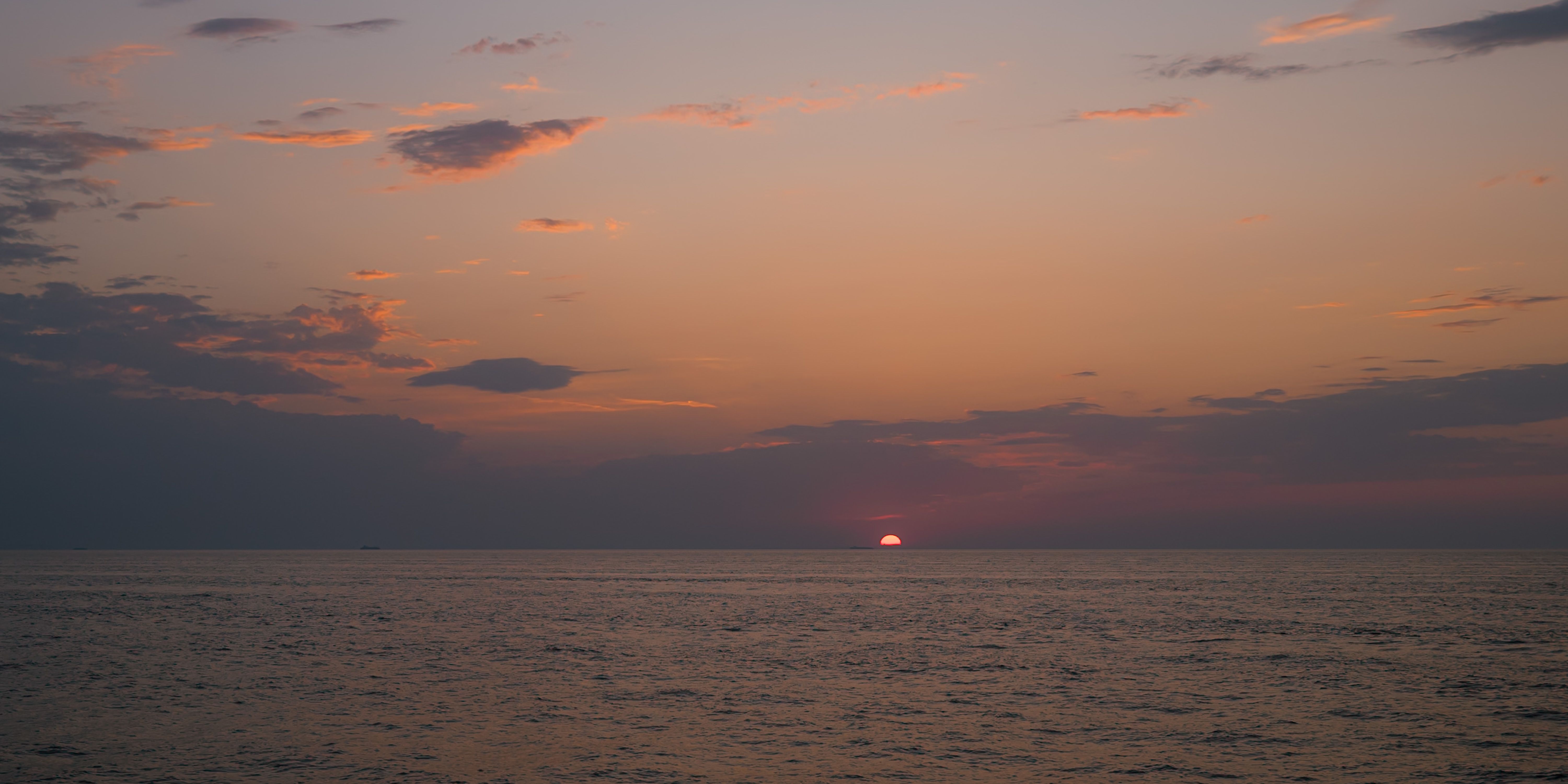 A sunset over the ocean with a boat in the distance · Free Stock Photo