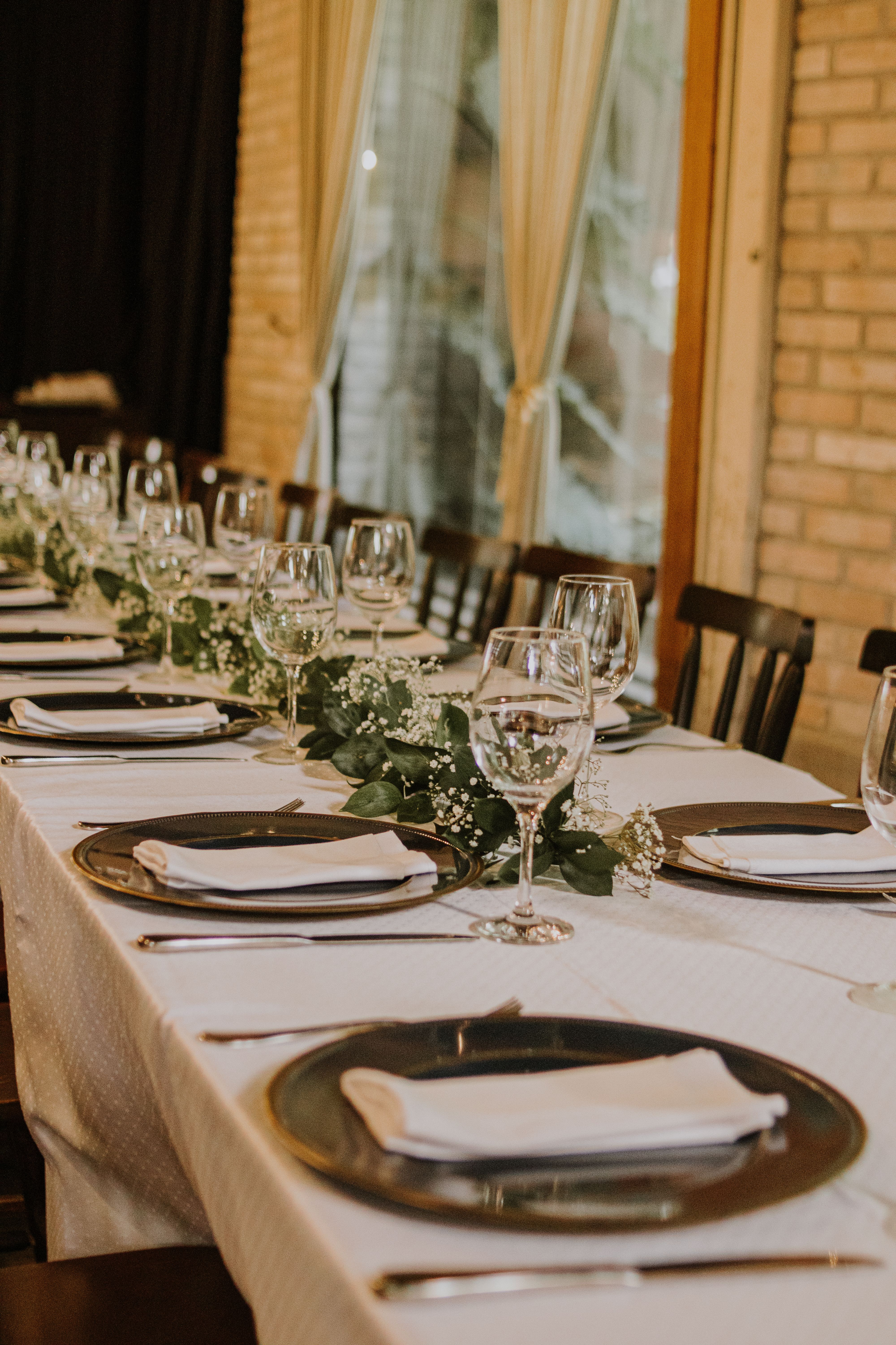A long table with white linens and greenery · Free Stock Photo
