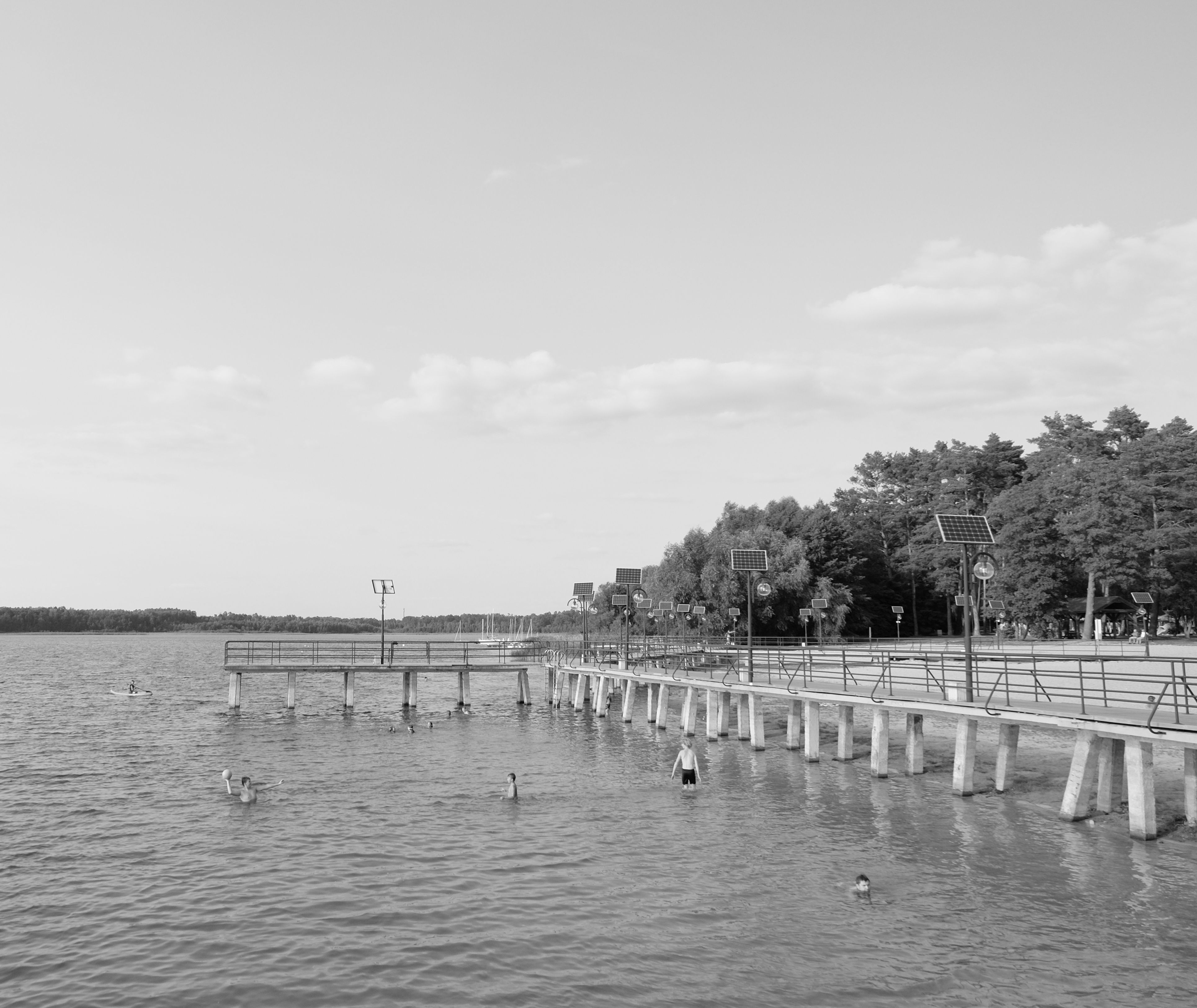 A black and white photo of a pier with people swimming · Free Stock Photo
