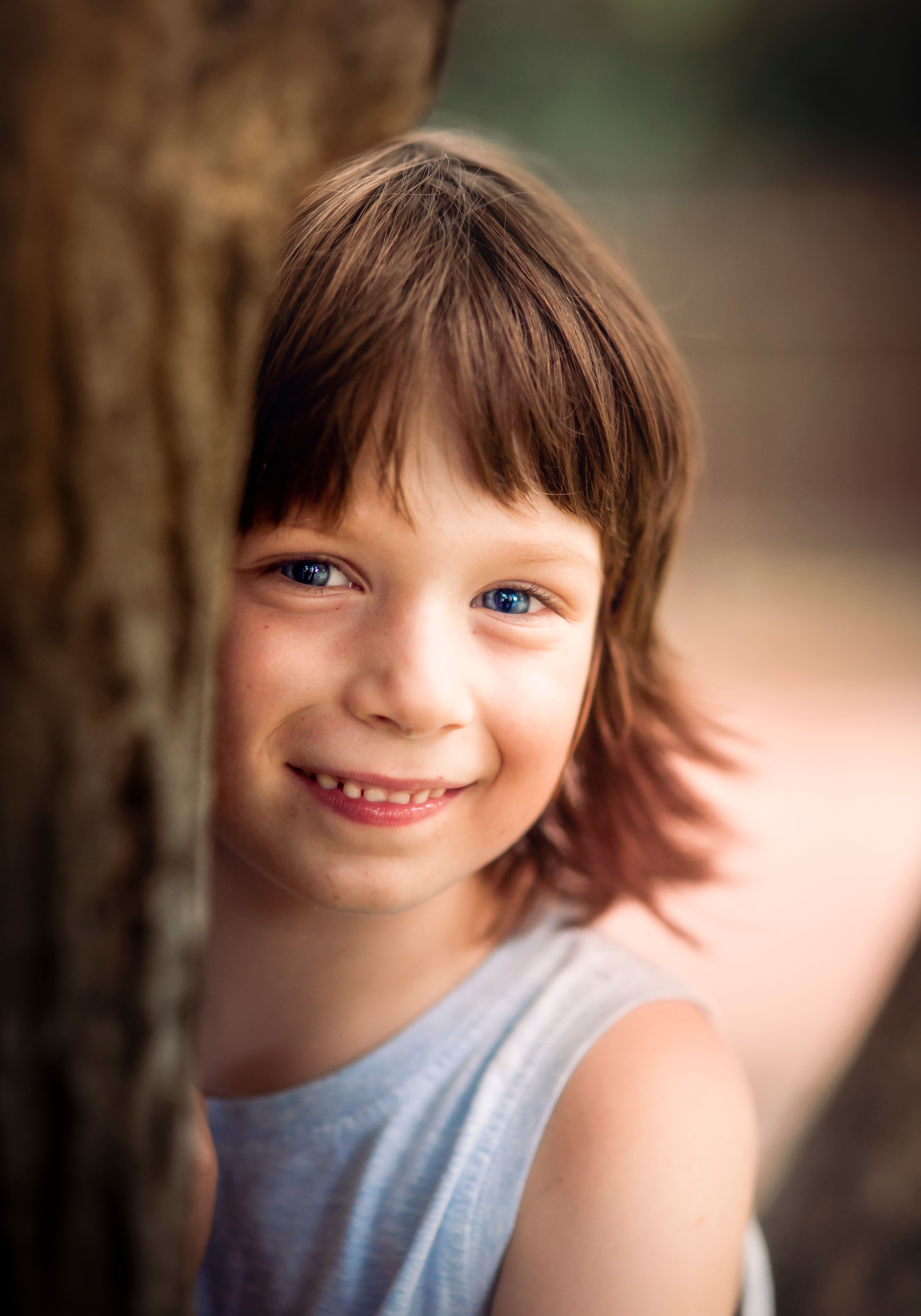 A young boy smiles while leaning against a tree · Free Stock Photo