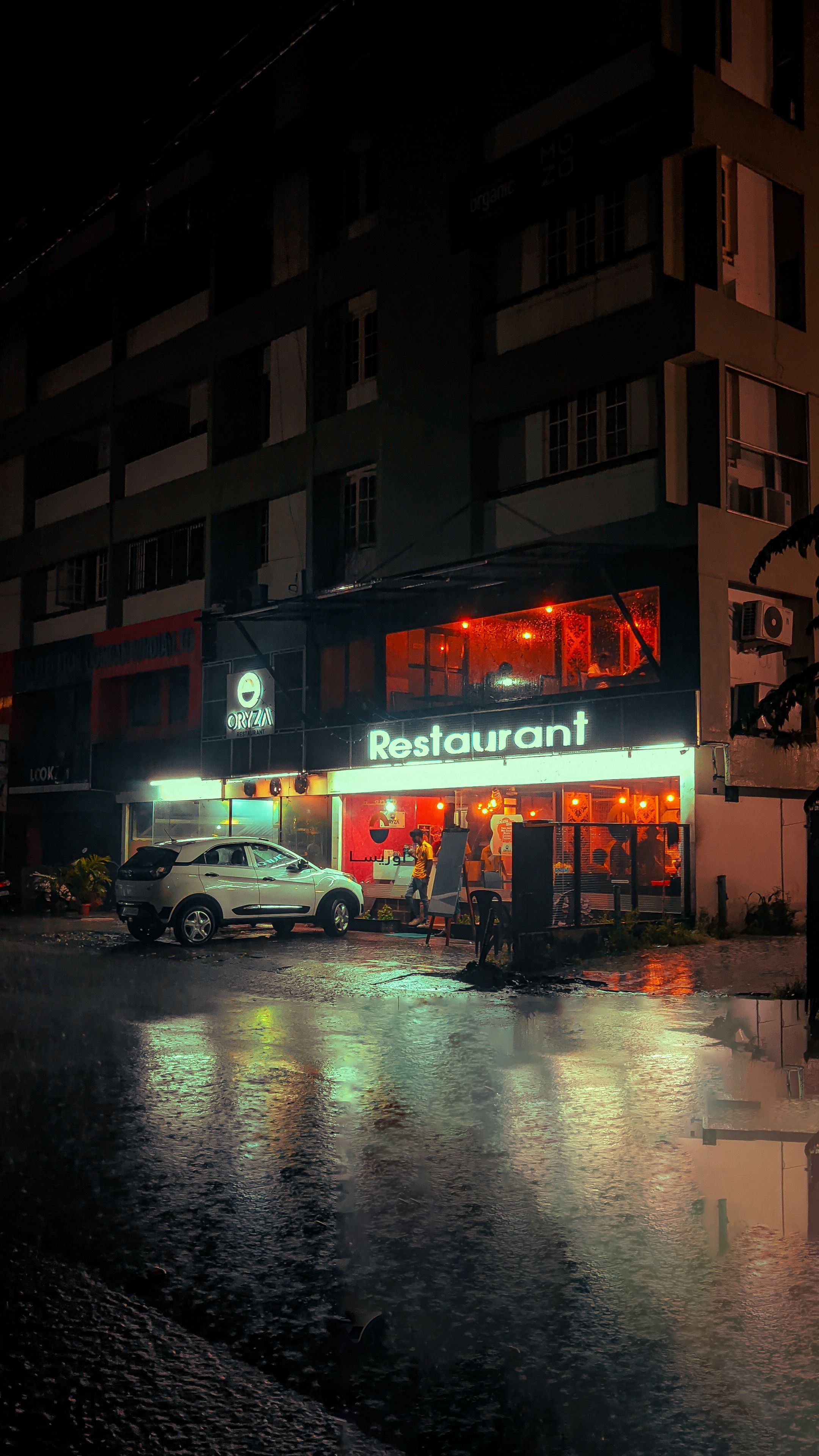 A restaurant is lit up at night in a rain · Free Stock Photo