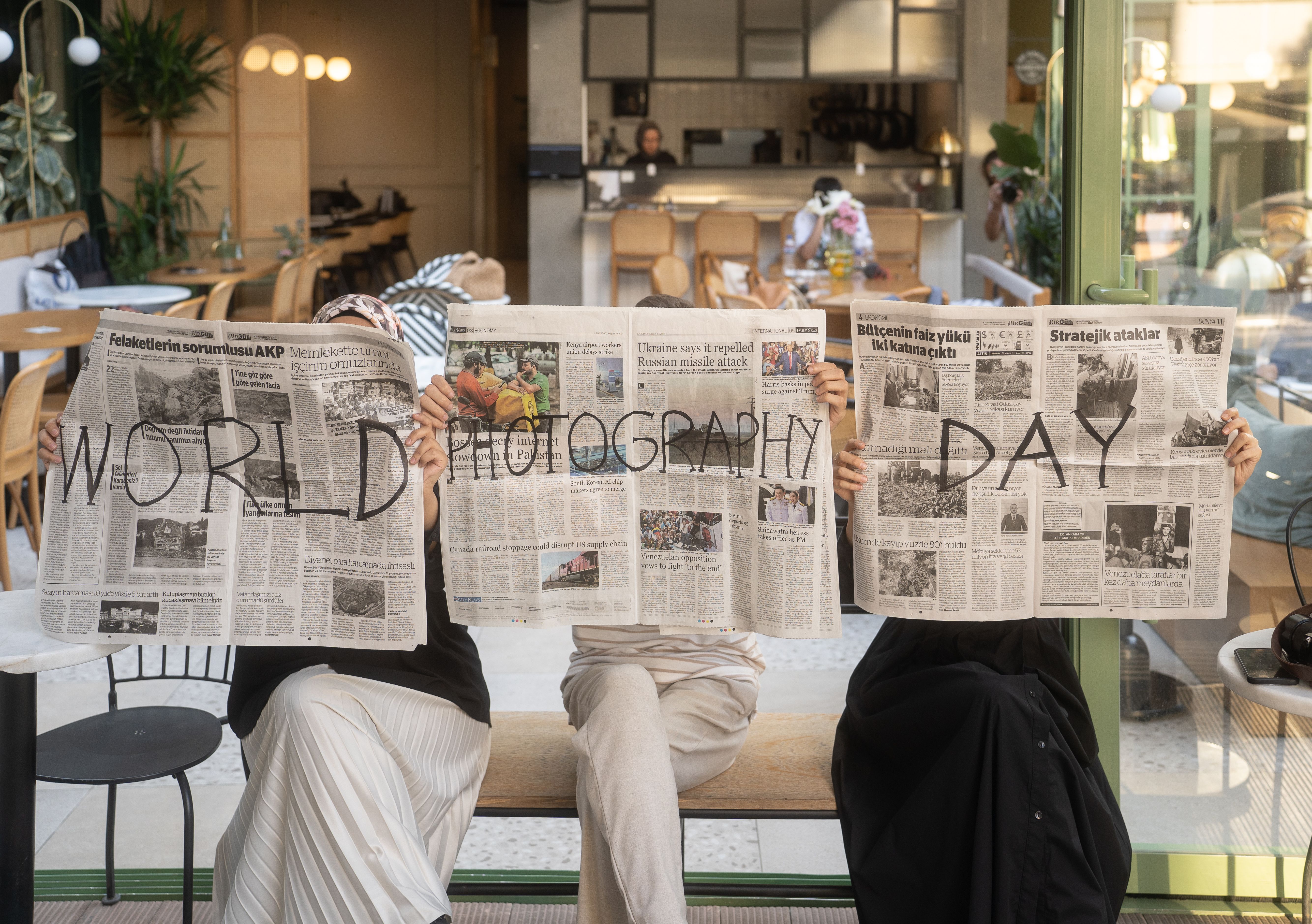 Three women sitting on a bench holding up newspapers · Free Stock Photo