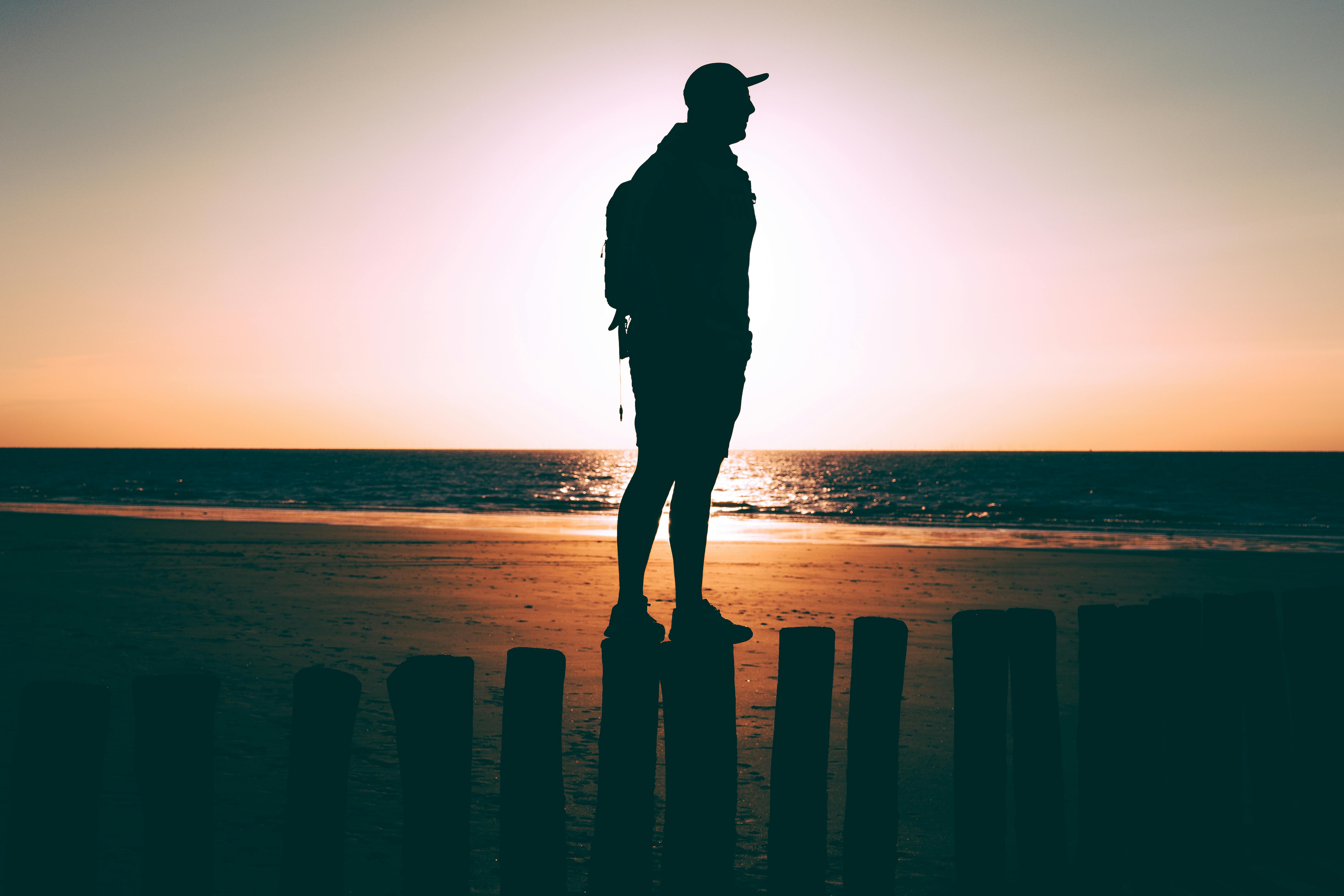 Man Standing On Posts On Seashore During Golden Hour · Free Stock Photo