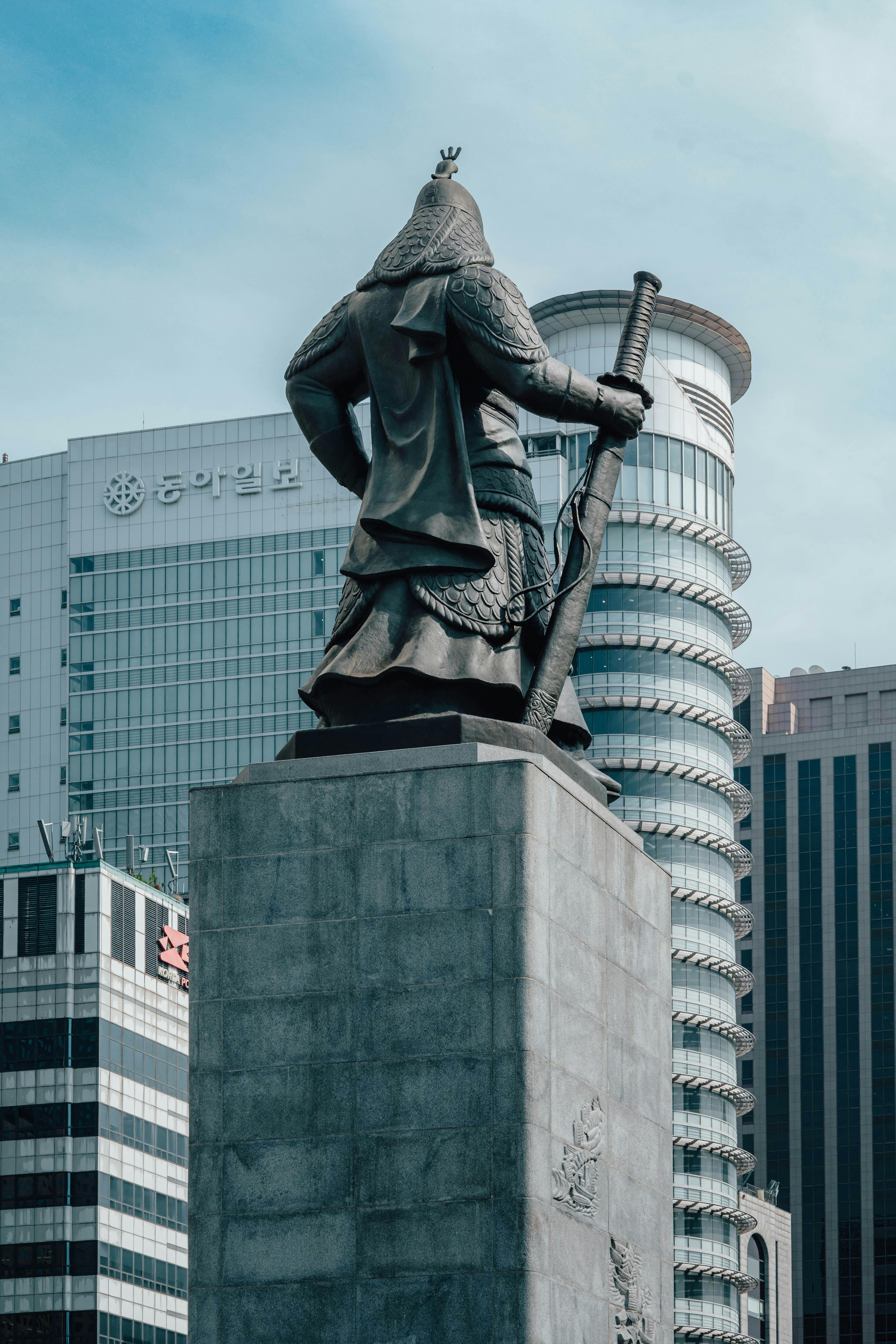A statue of a man with a sword in front of tall buildings · Free Stock ...