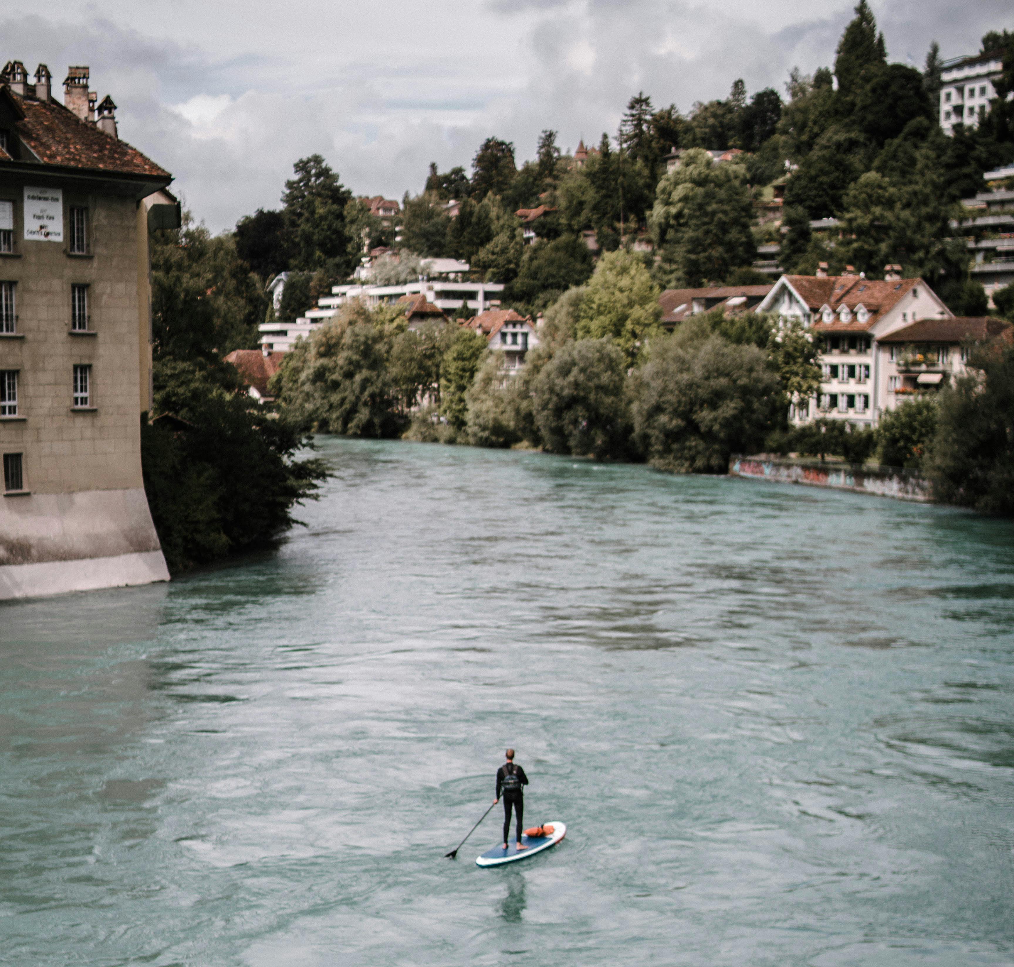 Man Paddling on Paddle Board Between Houses · Free Stock Photo
