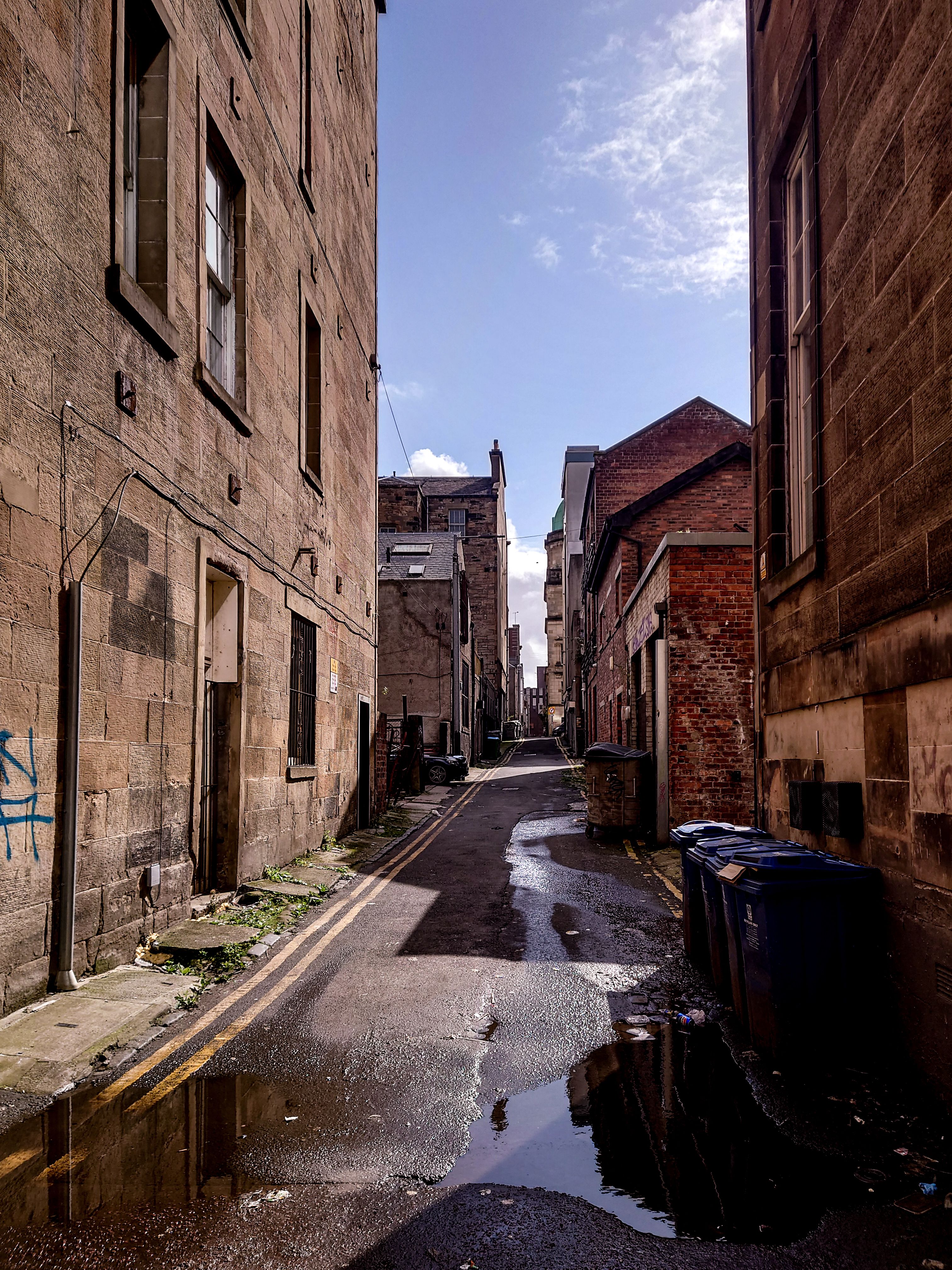 An alleyway with a water puddle and trash cans · Free Stock Photo