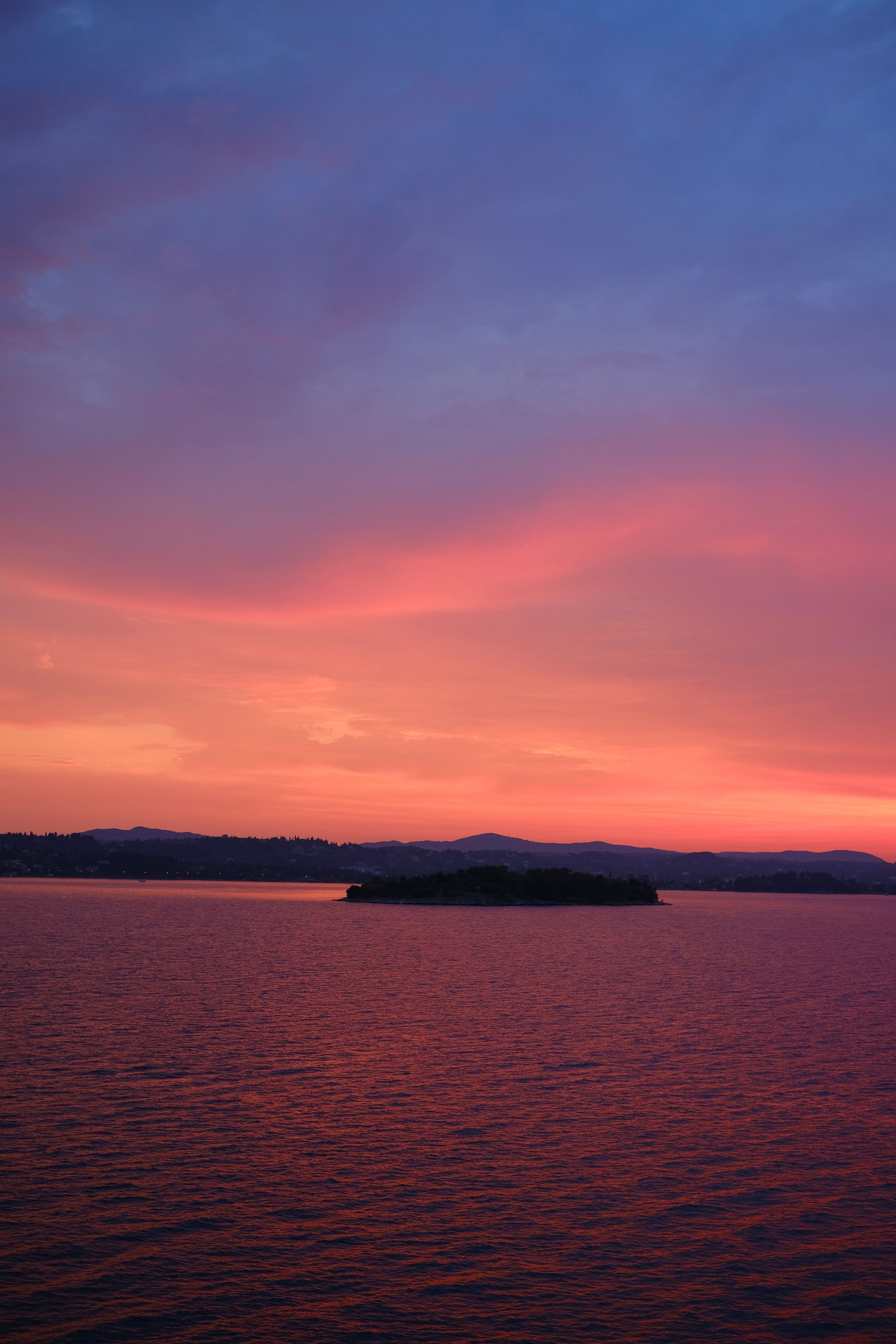 A sunset over a body of water with a small island in the middle · Free ...