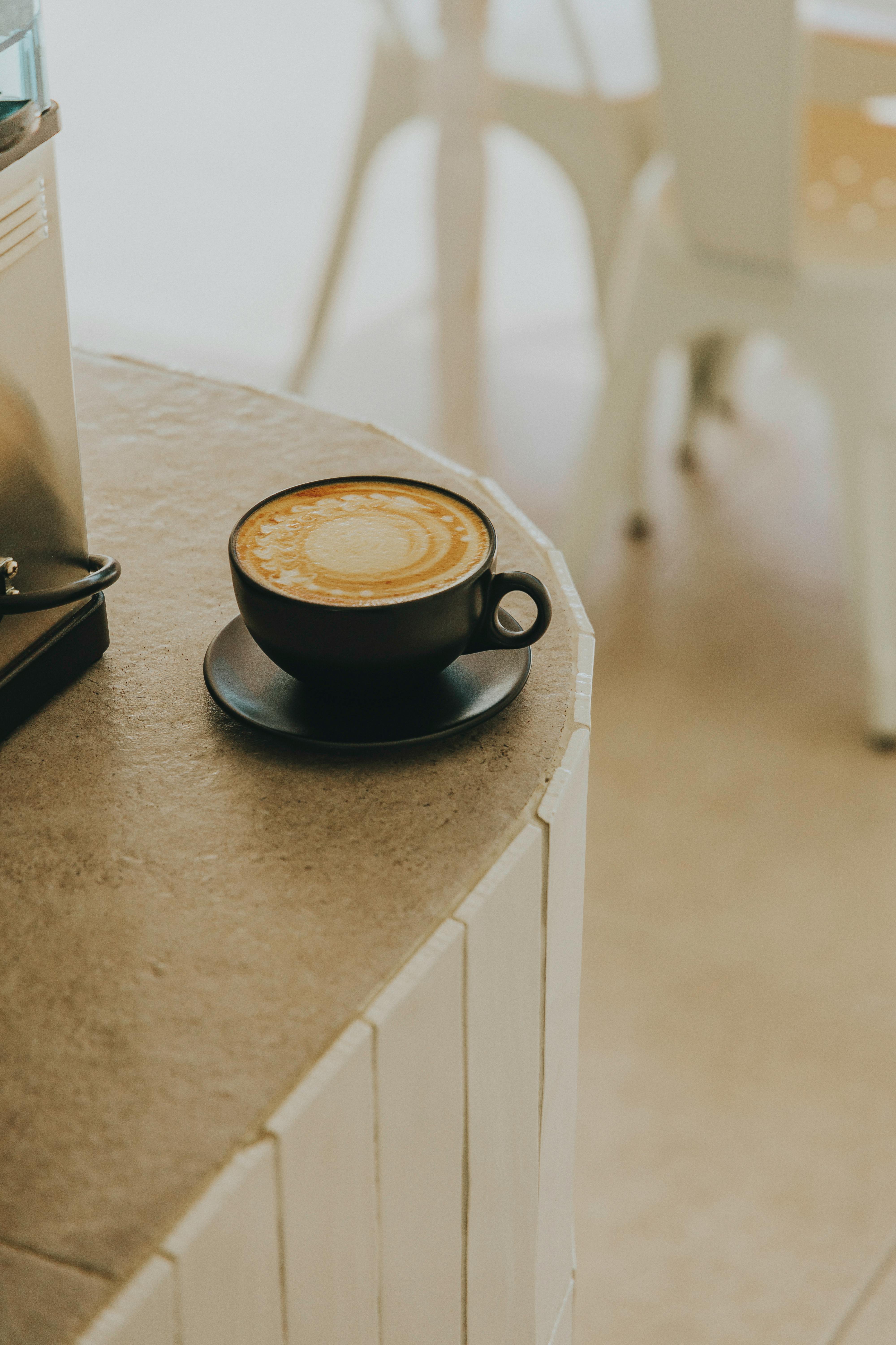 A cup of coffee sits on a counter next to a coffee machine · Free Stock ...