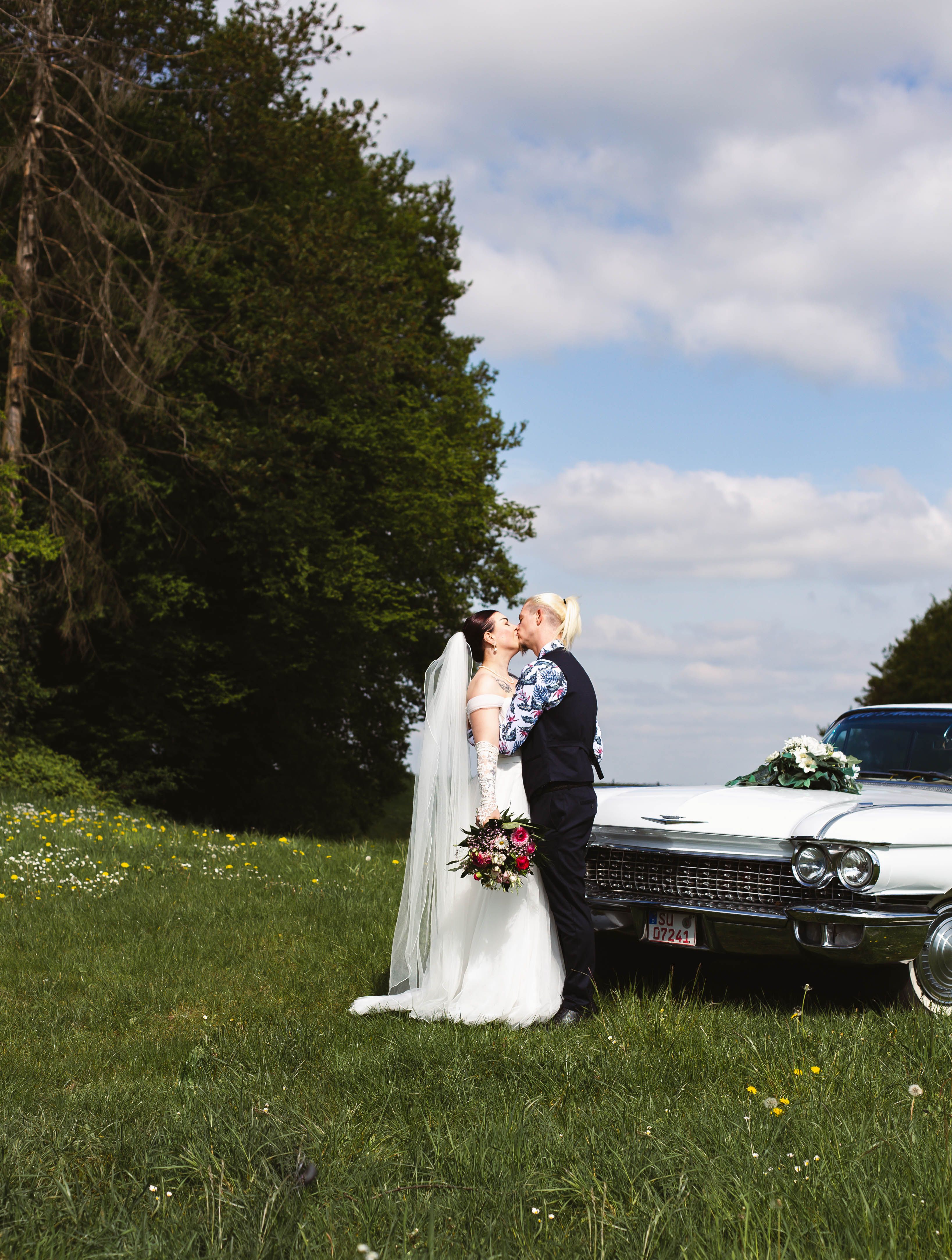 A bride and groom kiss in front of a classic car · Free Stock Photo