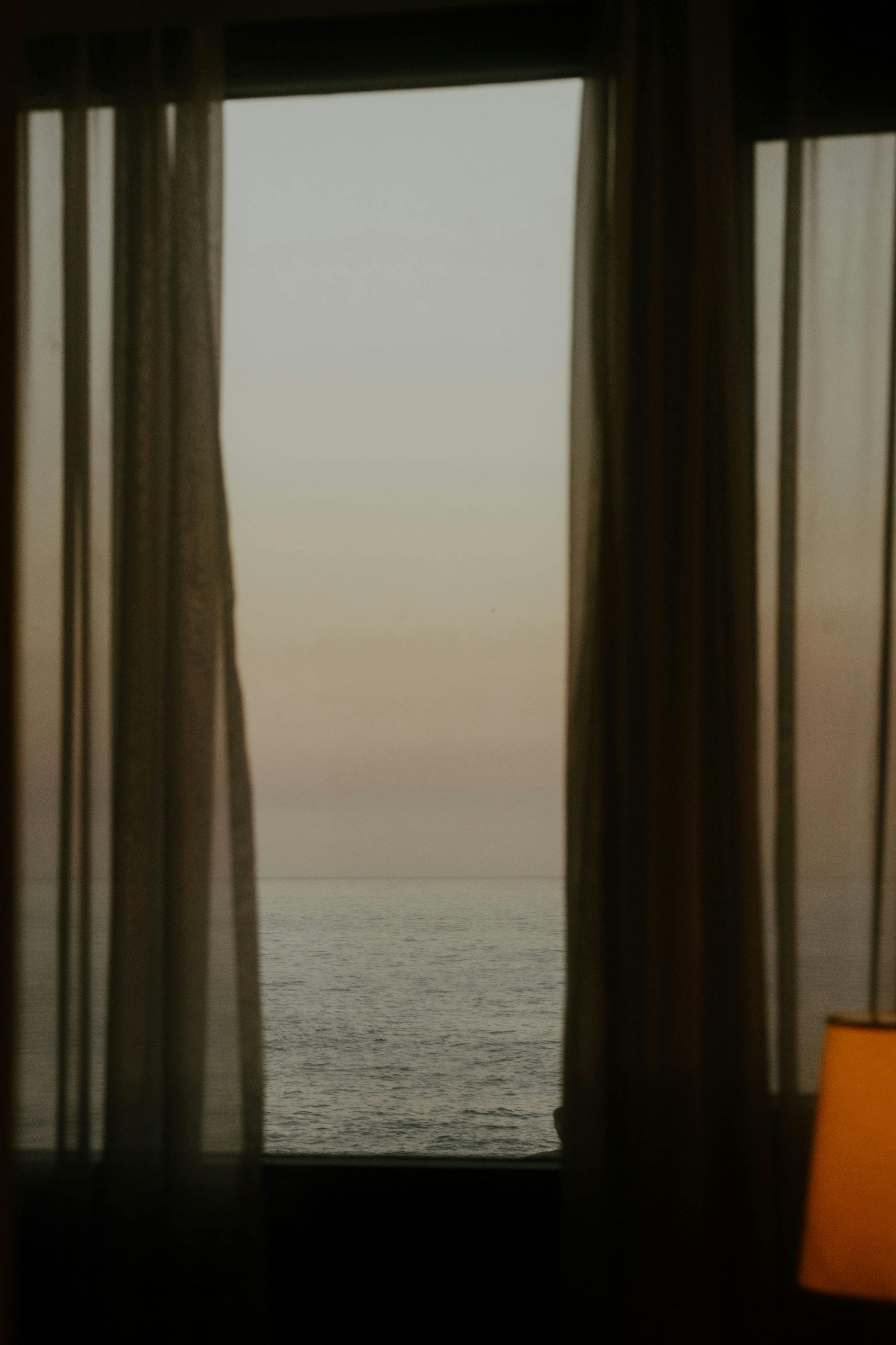 A view of the ocean from a window with curtains · Free Stock Photo
