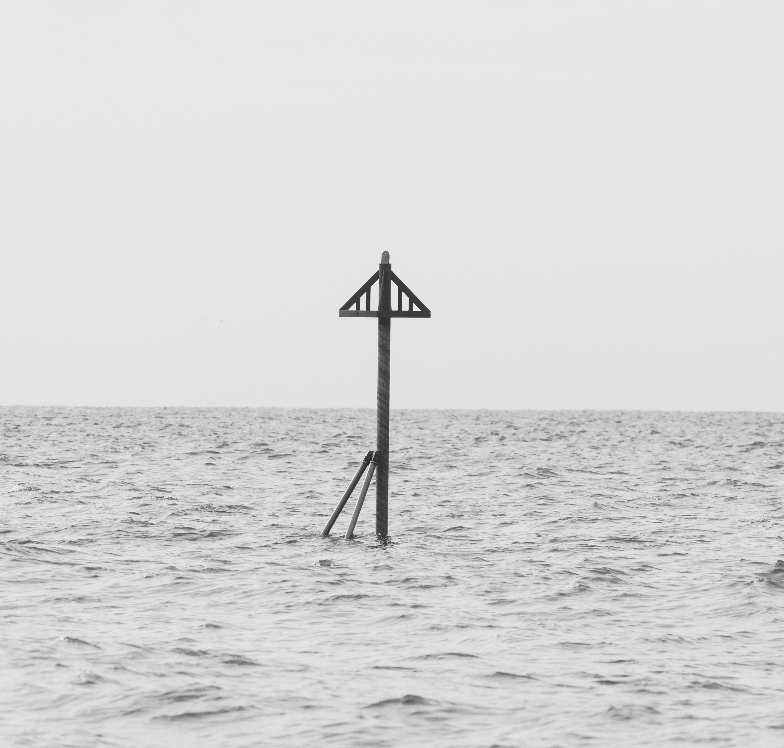 A black and white photo of a pole in the ocean · Free Stock Photo