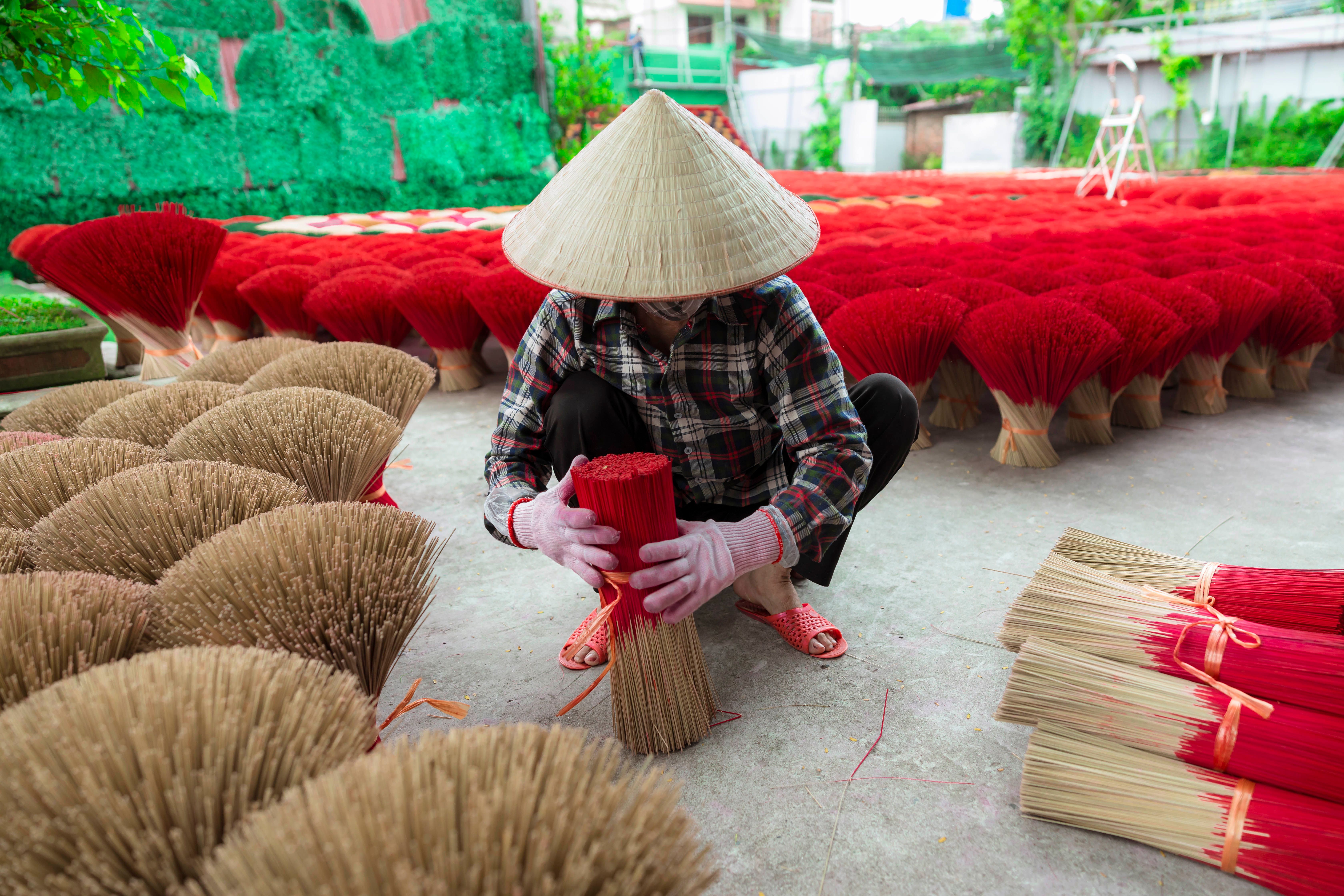 A woman is making straw hats with red and white straws · Free Stock Photo