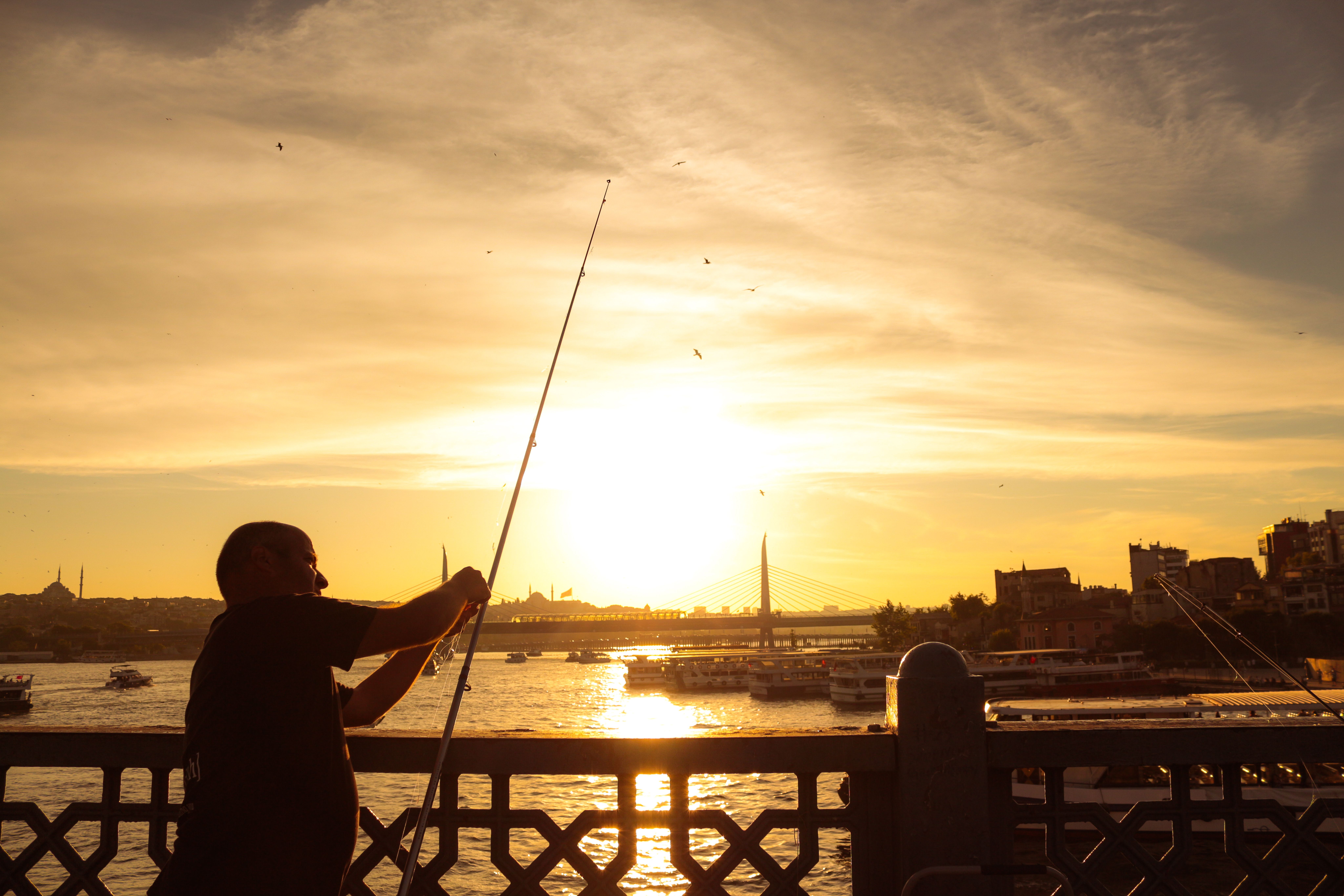 A man is fishing on a bridge at sunset · Free Stock Photo