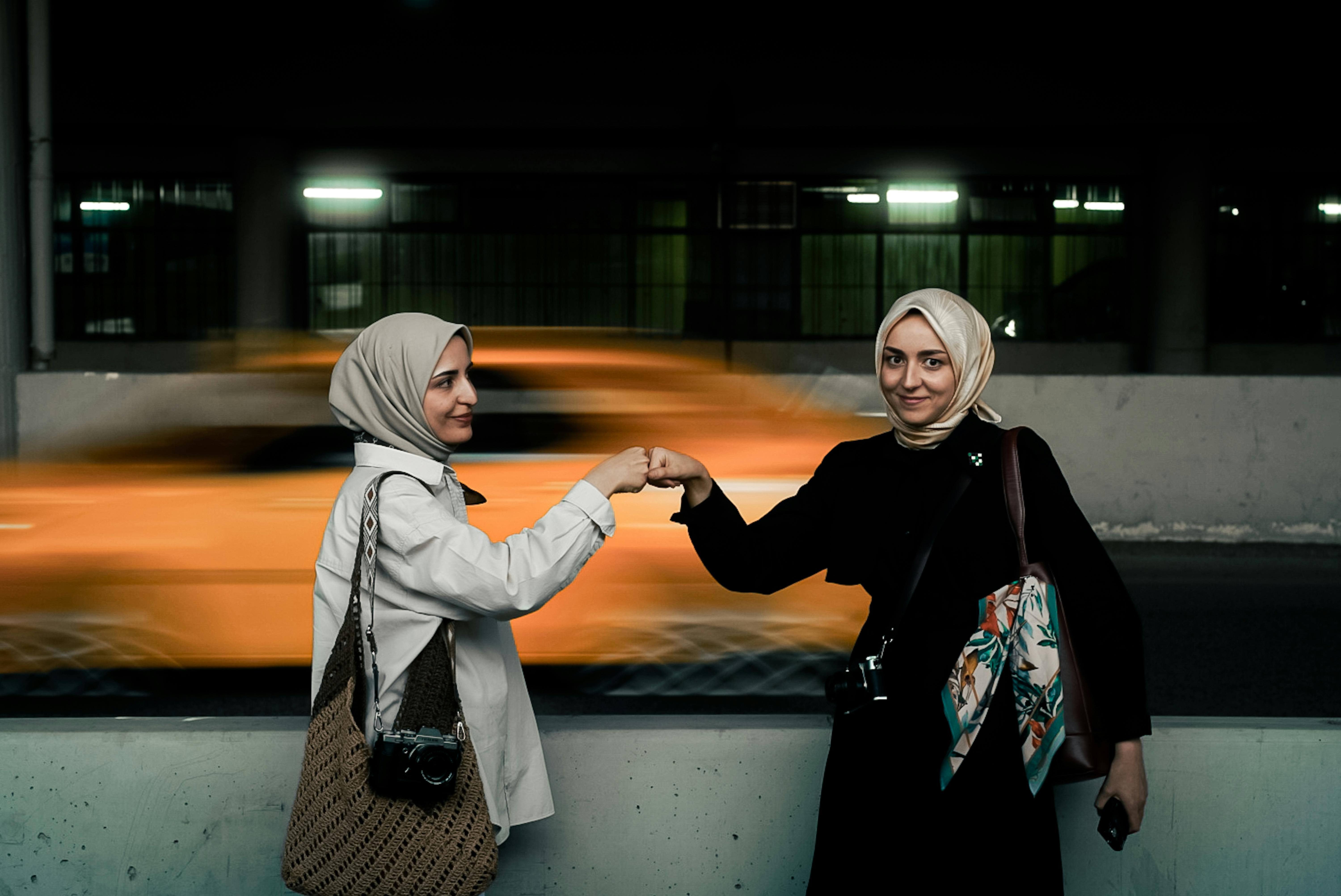 Two women in hijab holding hands in front of a taxi · Free Stock Photo