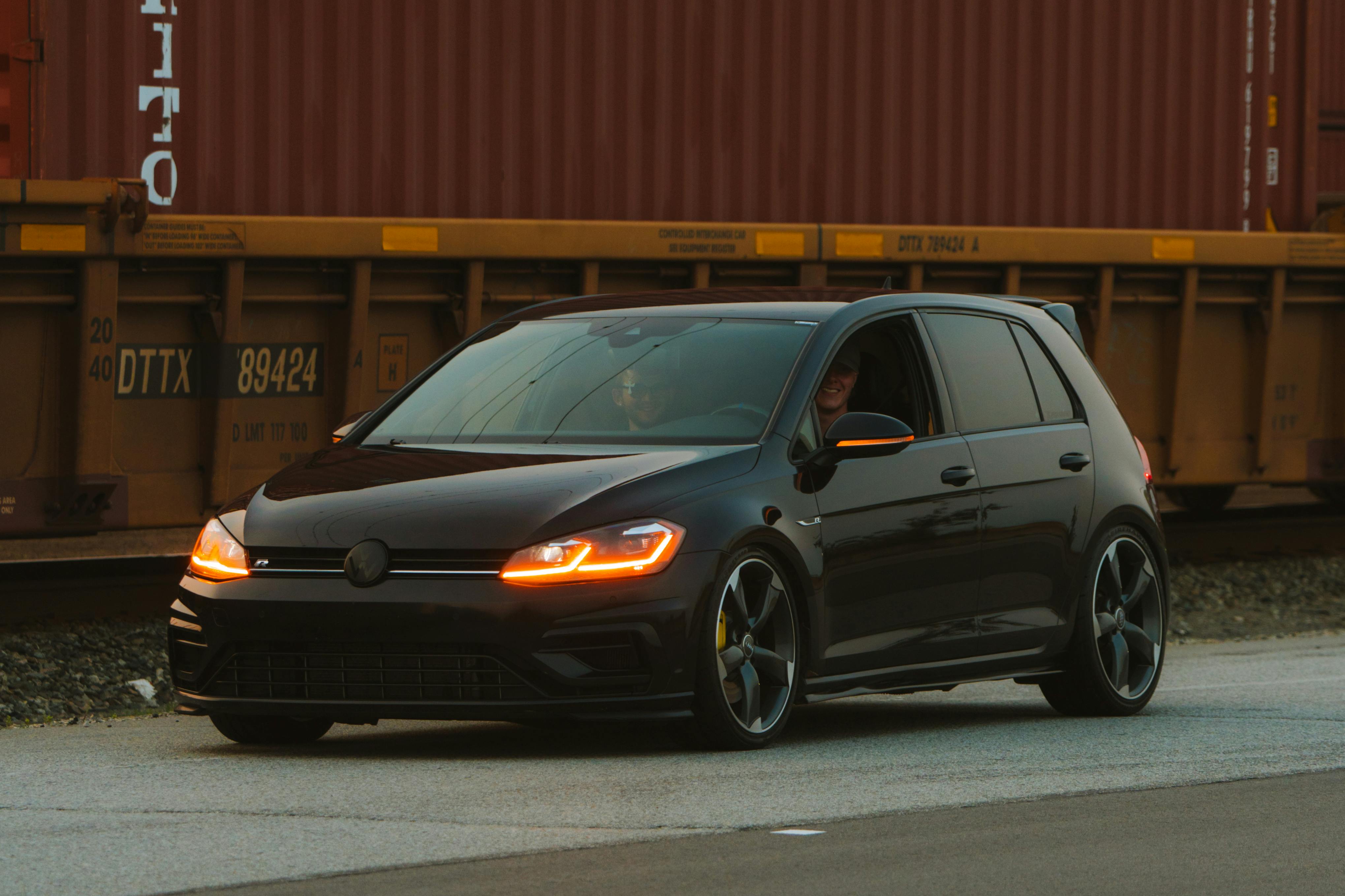 A black volkswagen golf r is parked in front of a train · Free Stock Photo