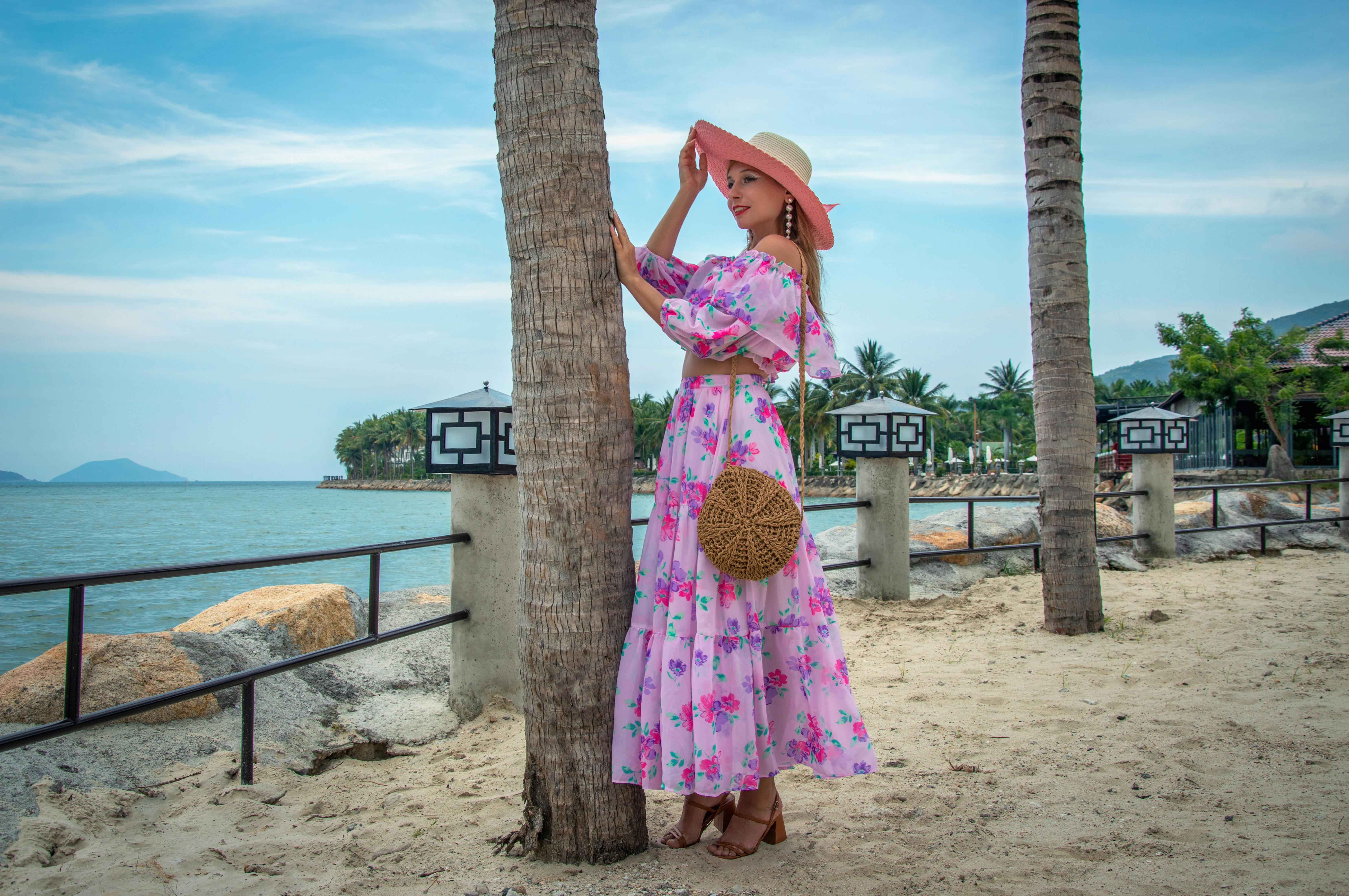 A woman in a pink dress is standing by a palm tree · Free Stock Photo