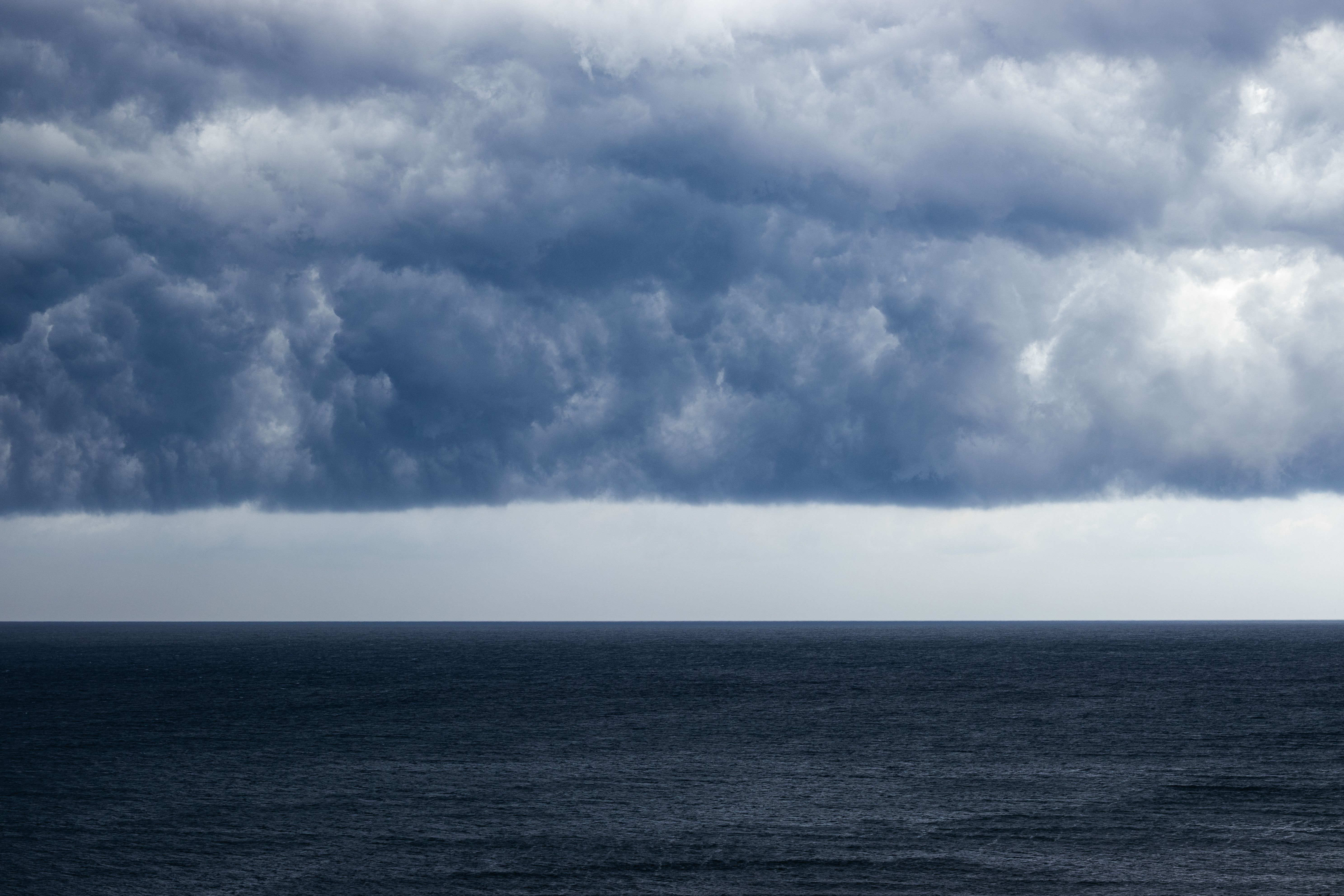 A stormy sky over the ocean with a boat in the distance · Free Stock Photo