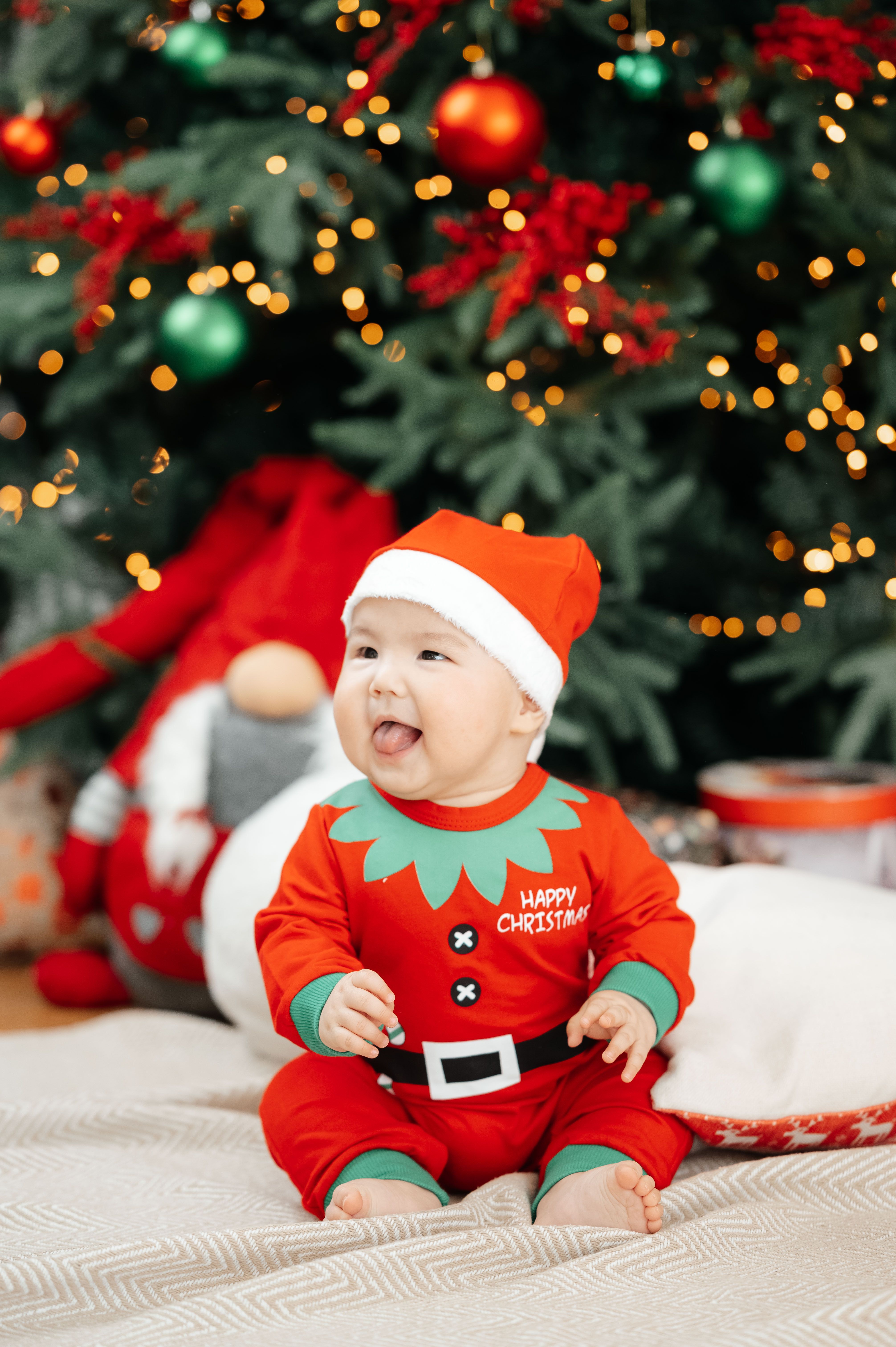 A baby in a red and green elf outfit sitting on the floor · Free Stock ...