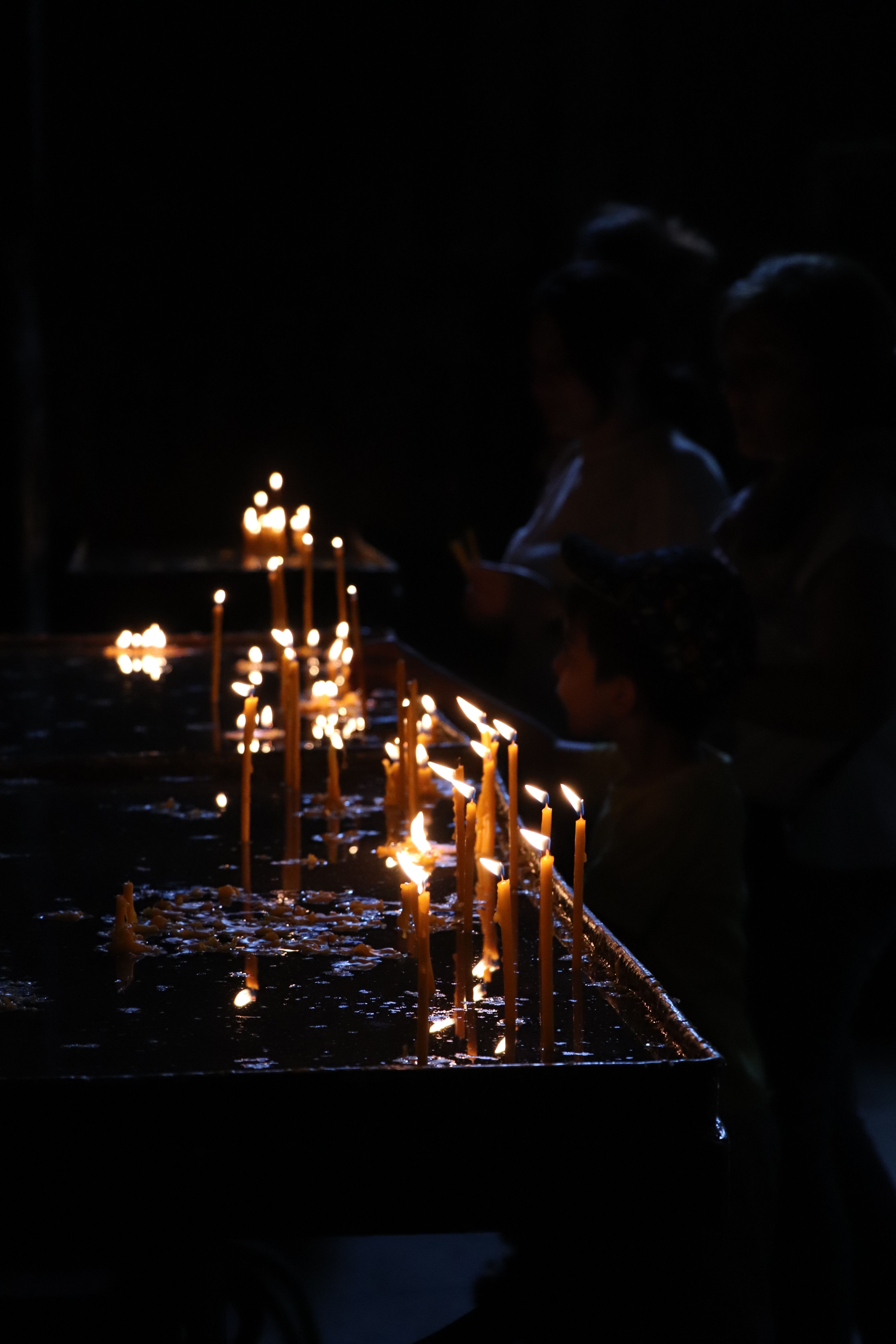 Candles are lit in a dark room with people standing around them · Free ...